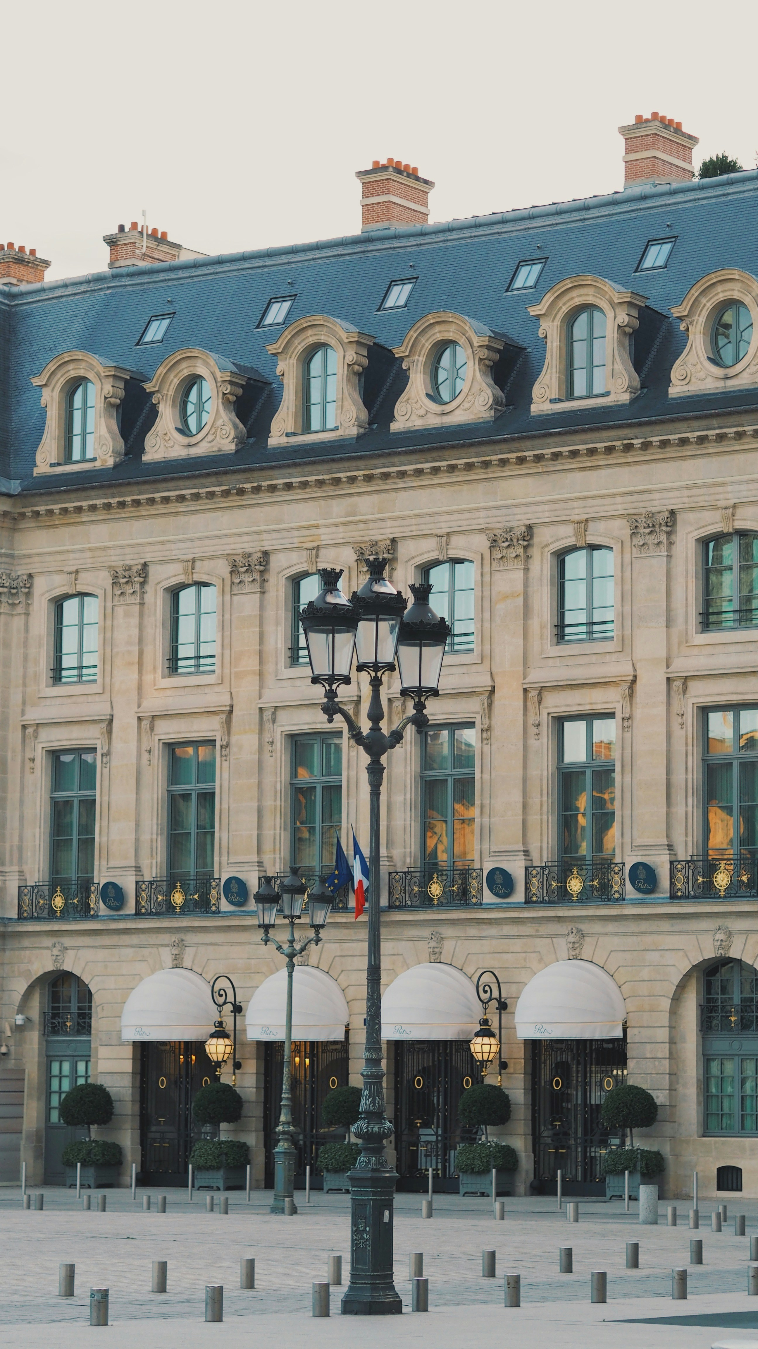Historic building façade adorned with decorative elements, featuring a classic street lamp and French flag in the foreground.