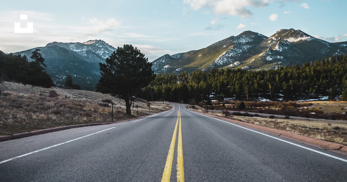 昼間の青空の下、緑の木々と山の近くの灰色のコンクリート道路の写真 Unsplashの無料青い写真