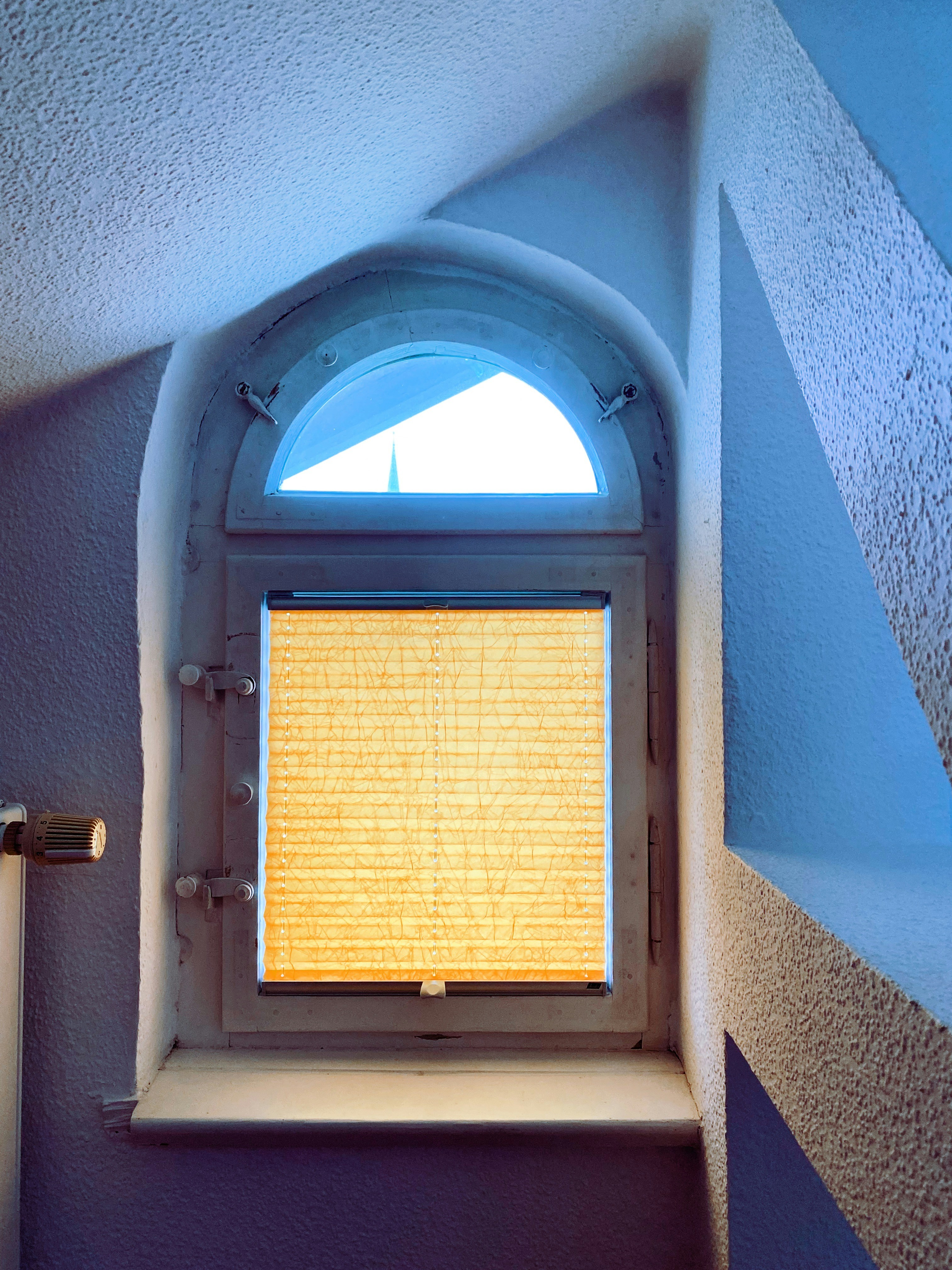 Amber Blind Framing a Vaulted Attic Window Against Blue Textures