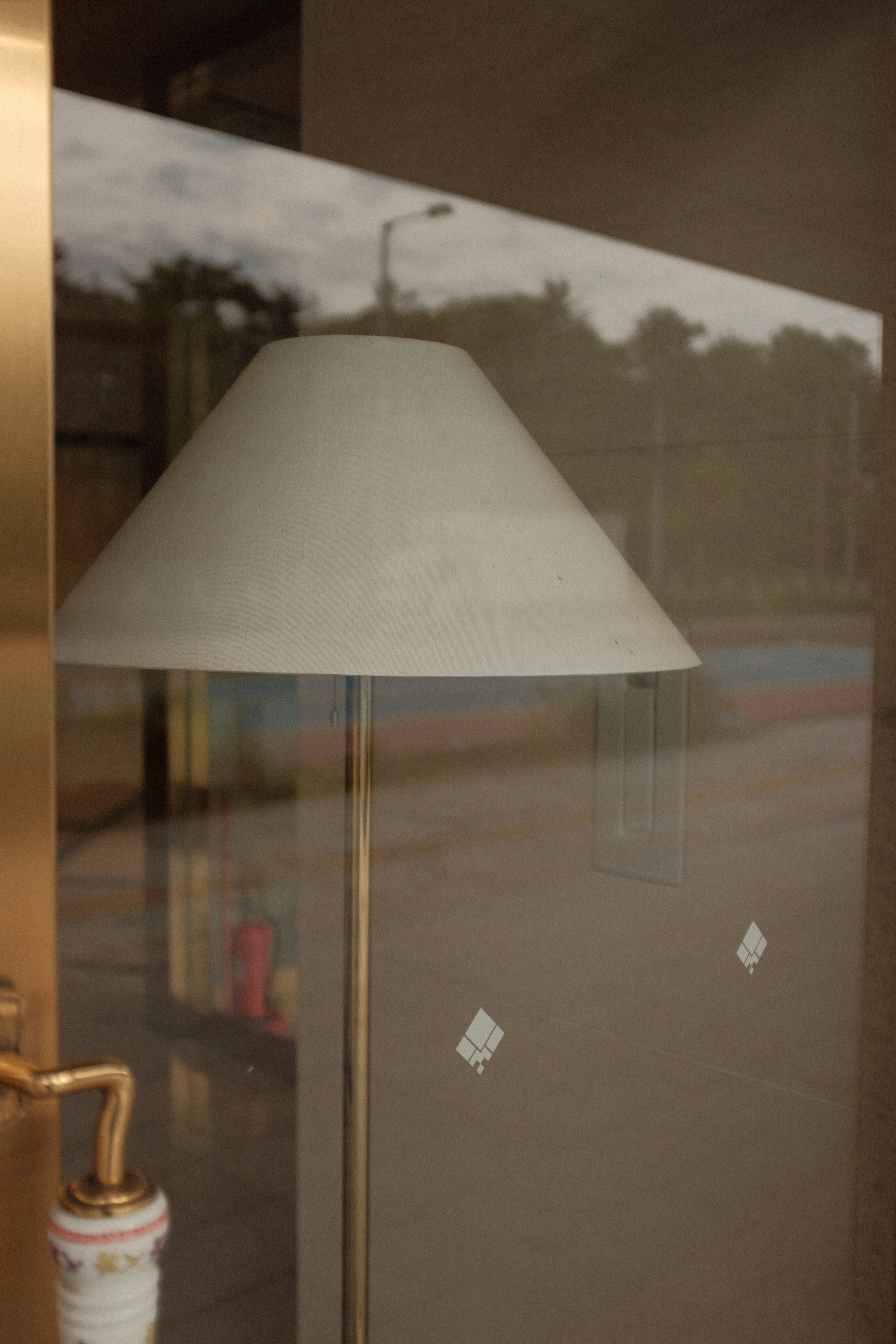 A minimalist lamp reflected in a glass door with subtle geometric designs. The scene captures the interplay of light and reflection.