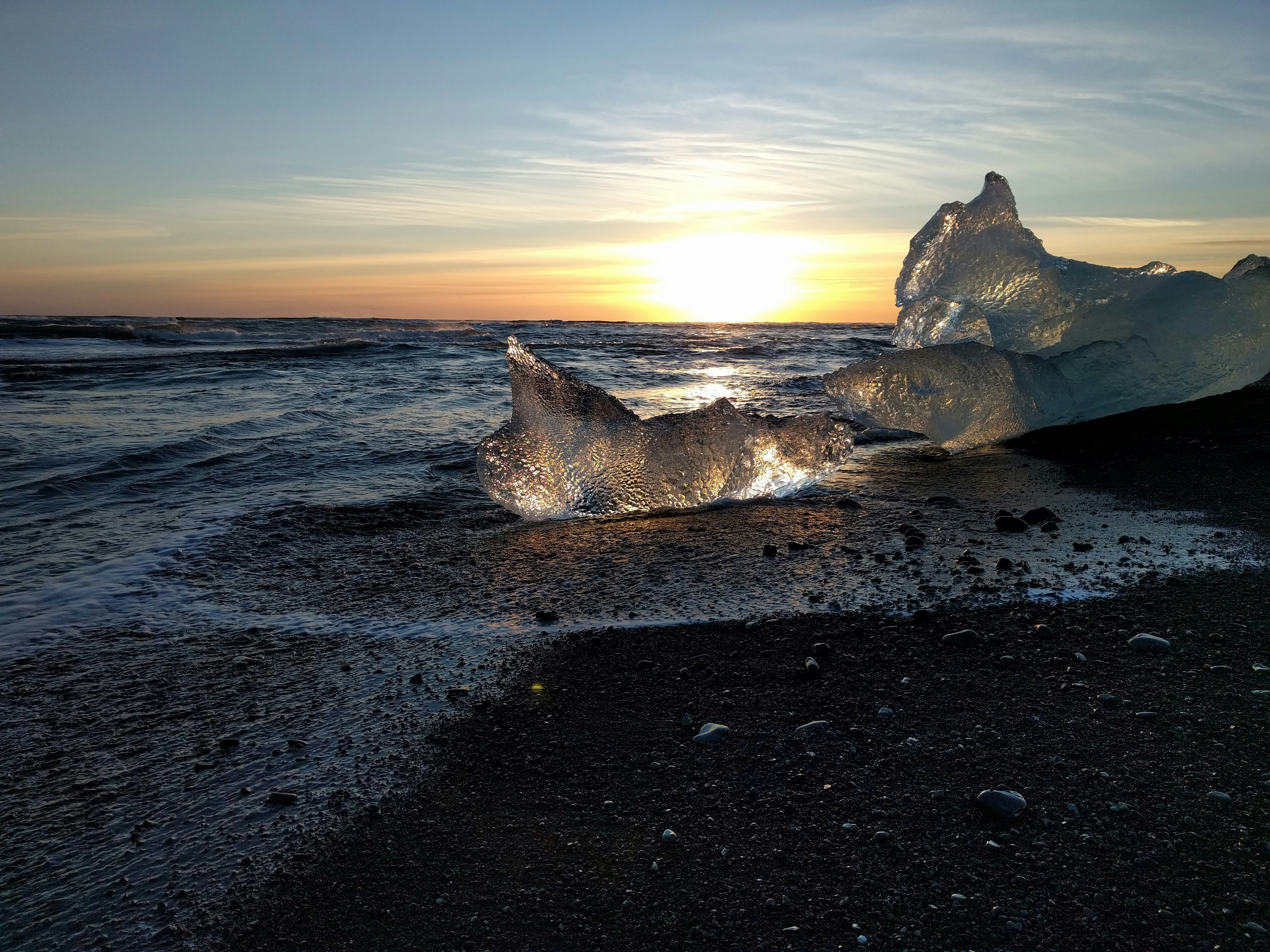 Ice formations glimmering on a black sand beach with the sun setting on the horizon.