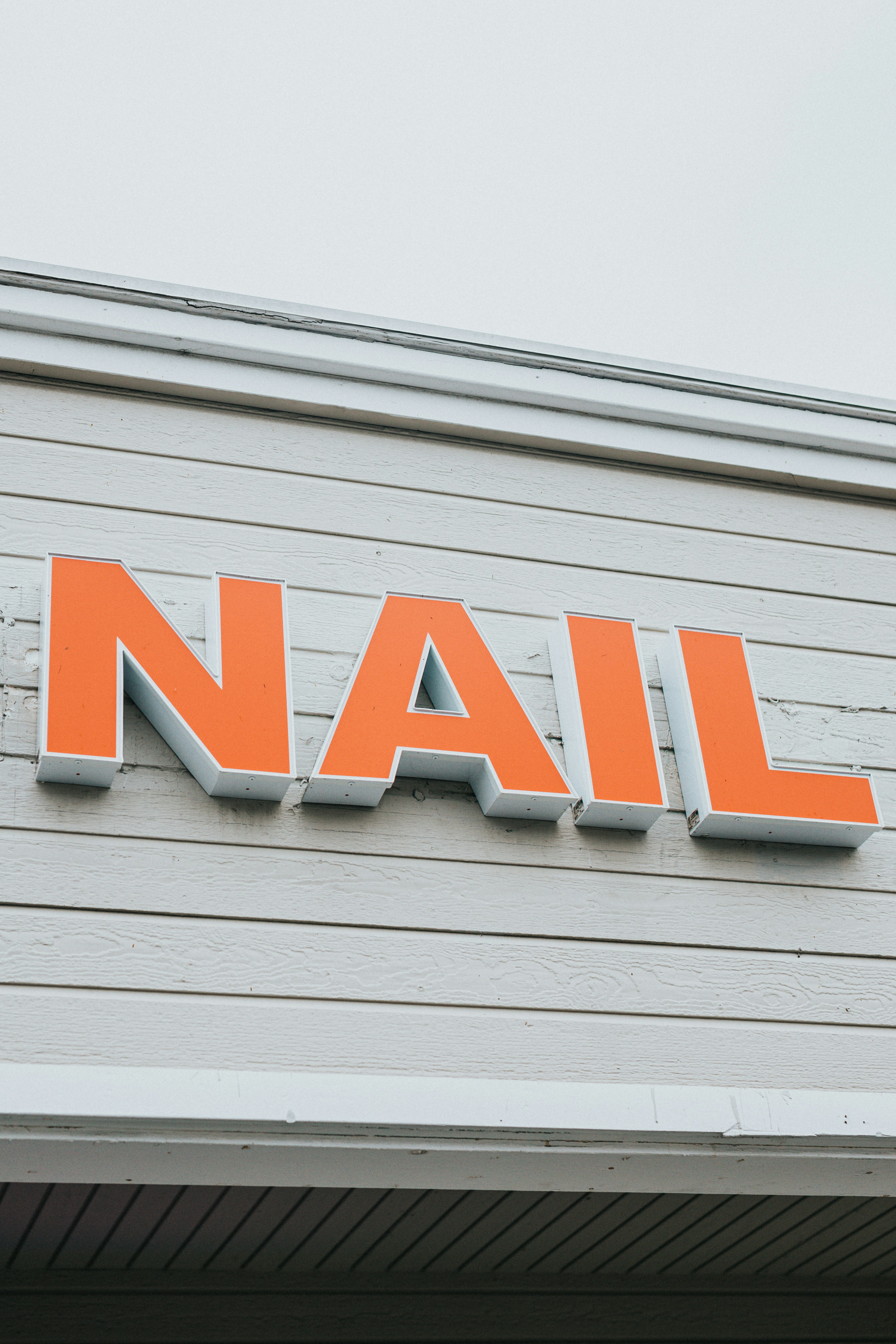 An orange nail sign on the side of a building photo – Free Logo Image ...