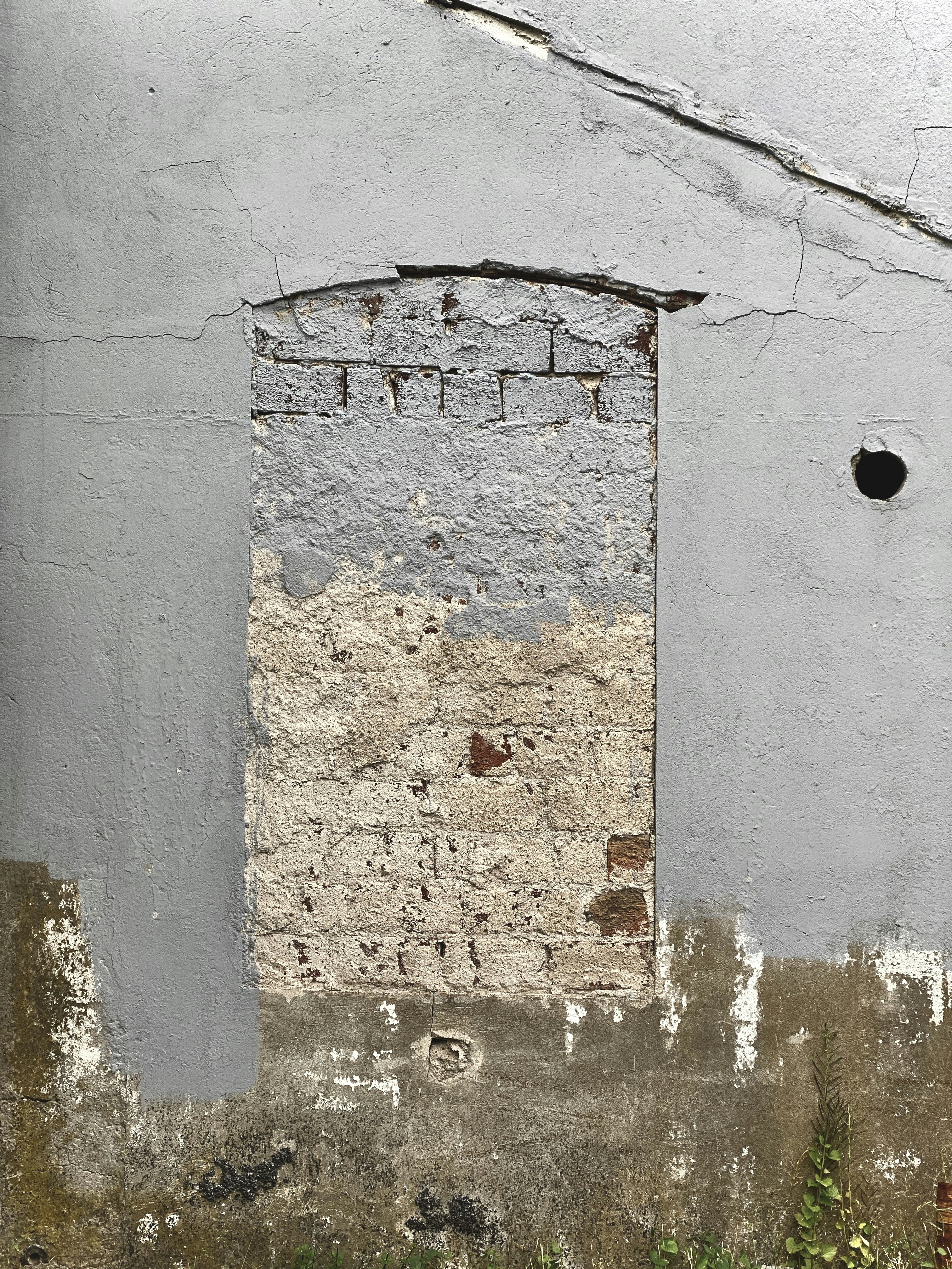 Weathered wall revealing layers of paint and brick, with a circular hole adding intrigue. Flaking textures and muted colors tell a story of time and neglect.