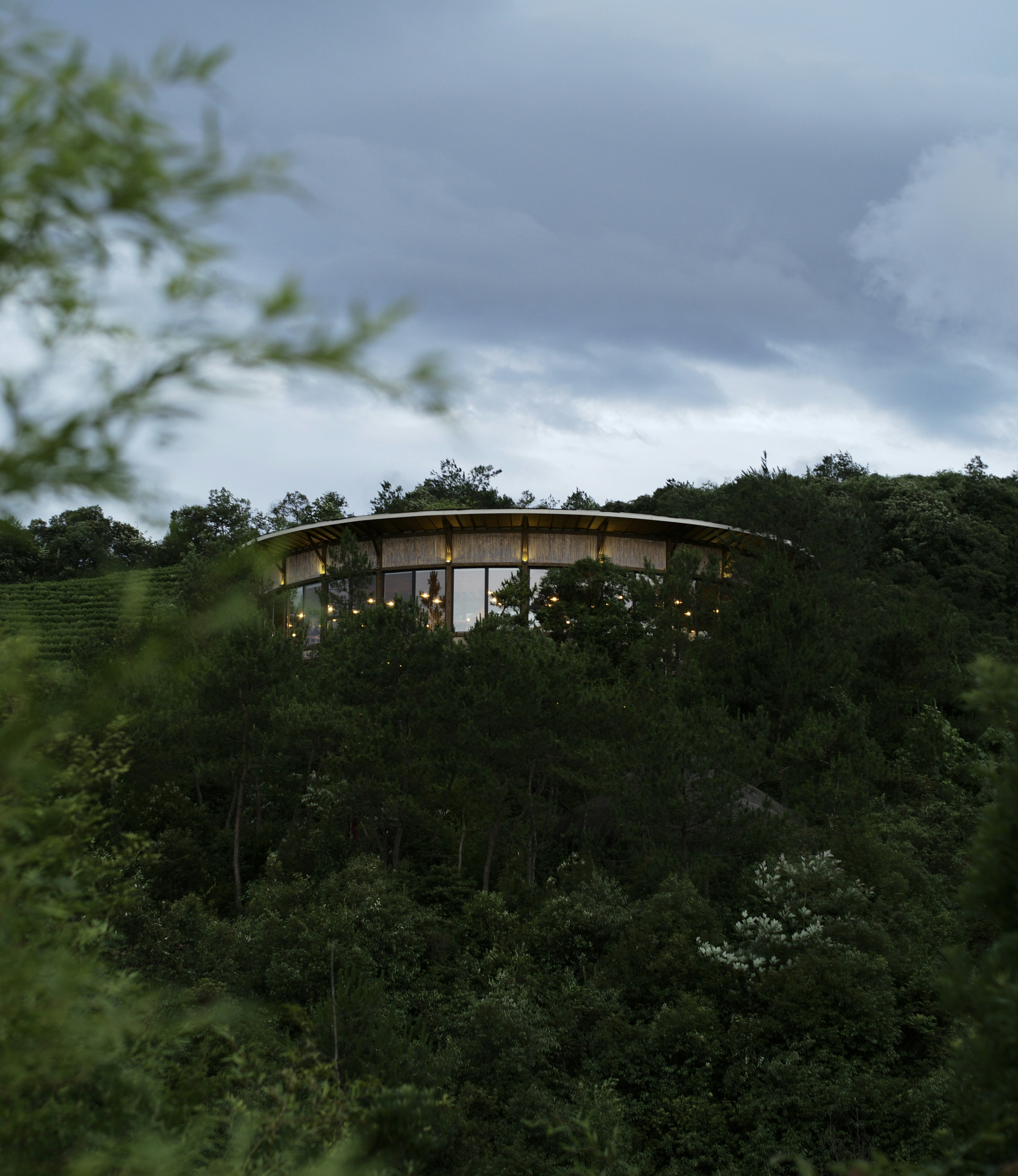 Circular building nestled among lush green hills under a cloudy sky.