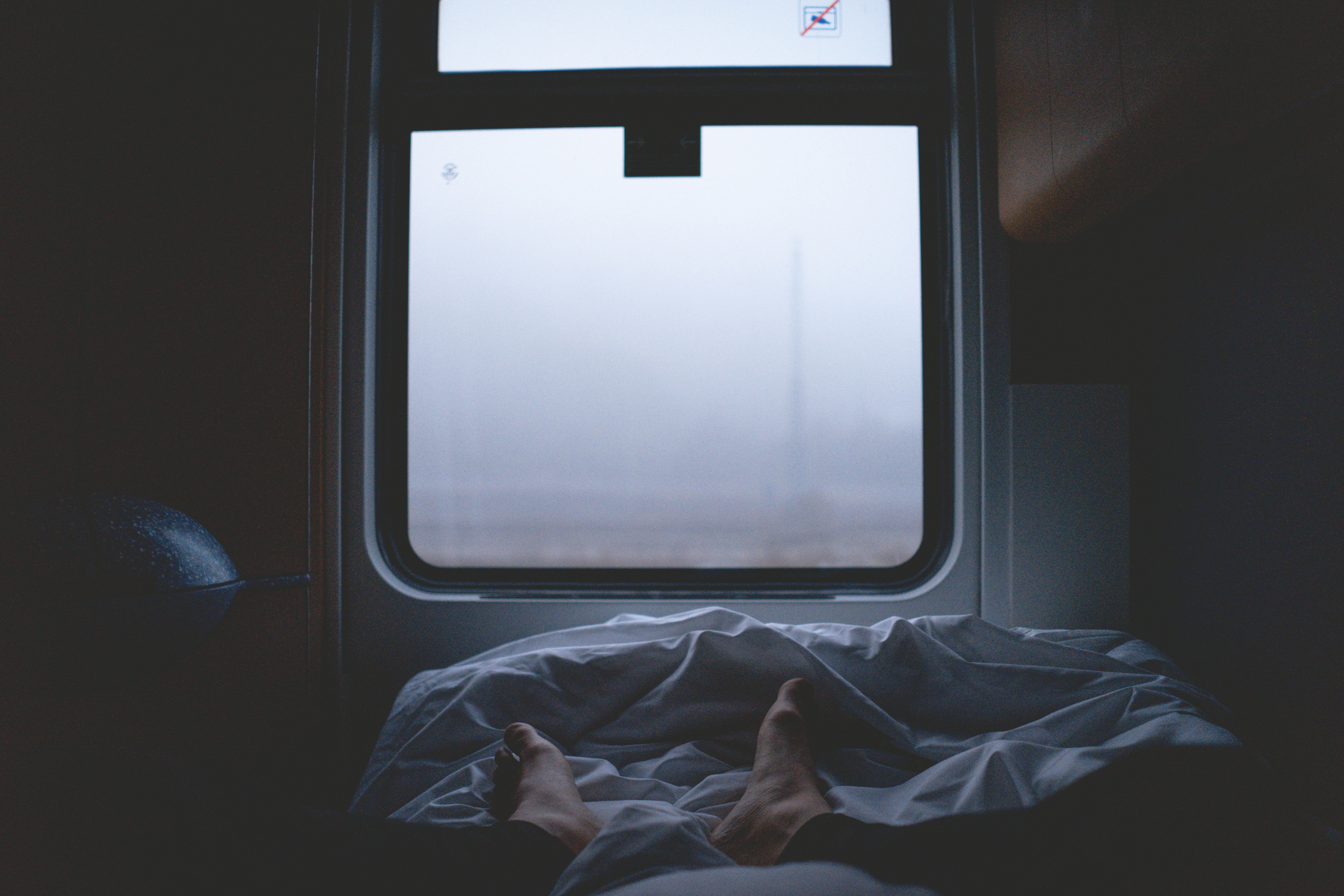 Cozy bed with bare feet visible, framed by a foggy window, evoking a sense of tranquility and solitude.
