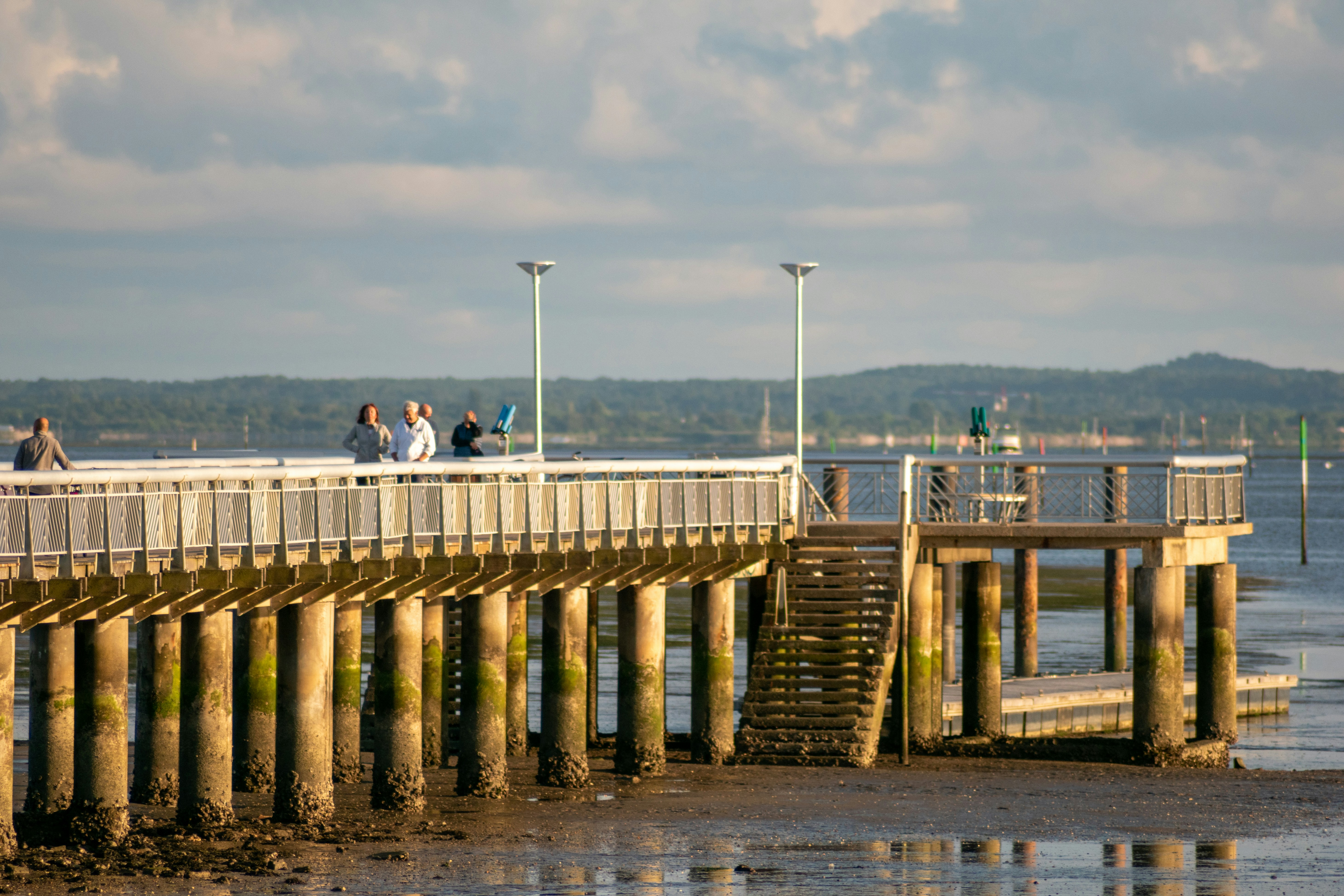 Sunlit Pier Ledger: Figures Pause Along a Calm Coastal Walkway