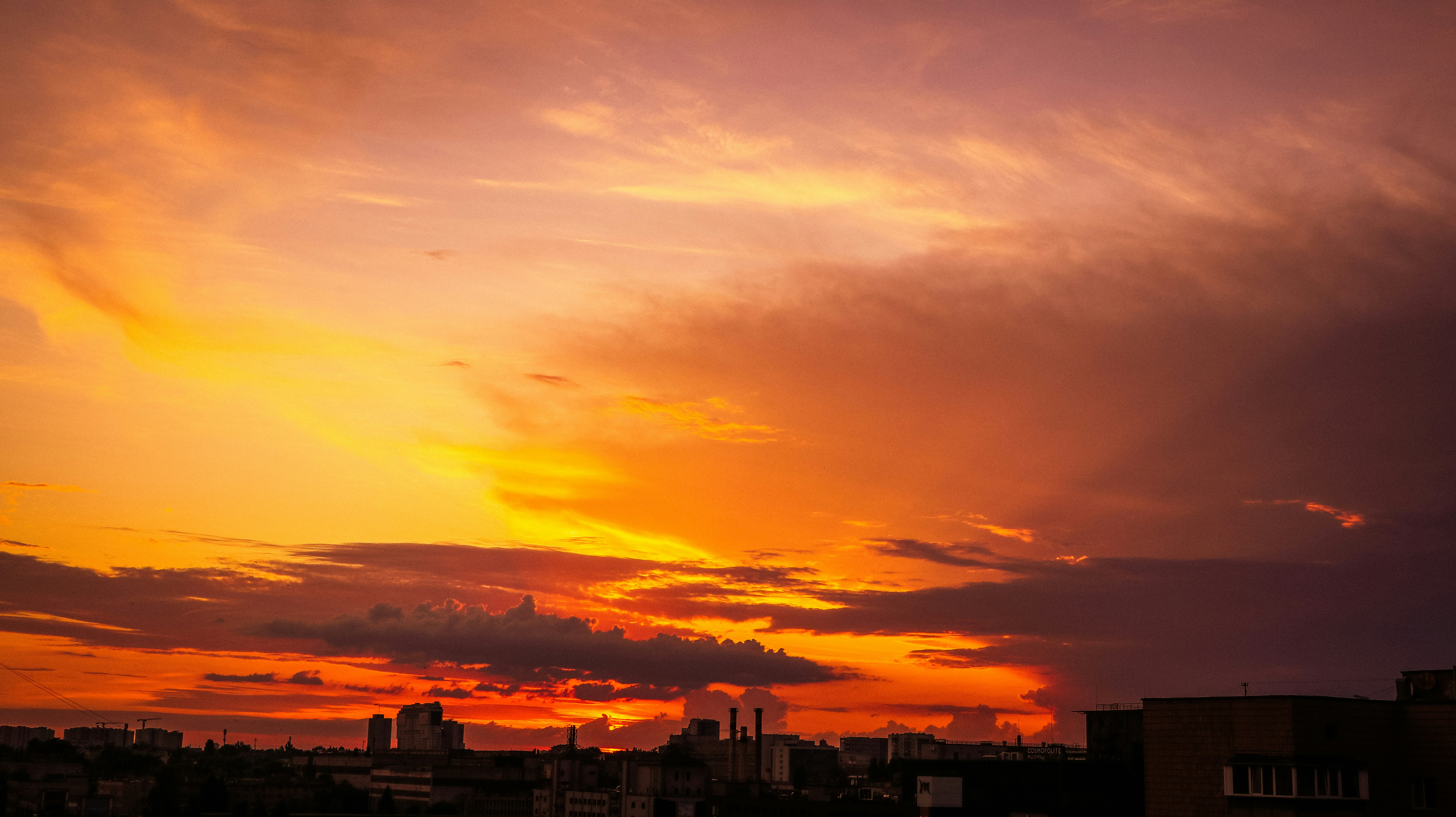 Vibrant sunset illuminating the sky with hues of orange and purple, casting a warm glow over city silhouettes.