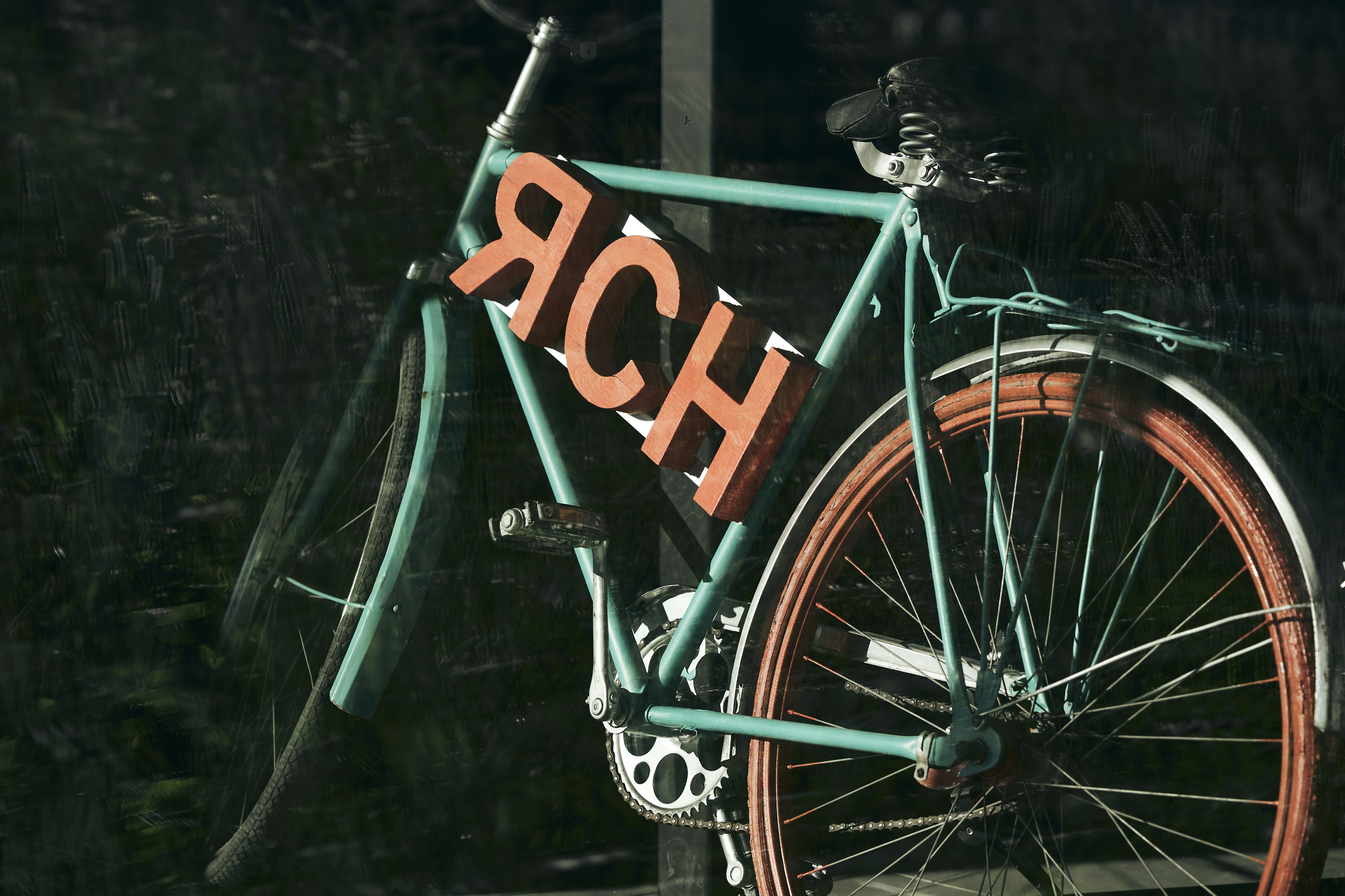 A retro bicycle adorned with a bold sign hangs against a dark backdrop, showcasing urban cycling aesthetics and creativity.