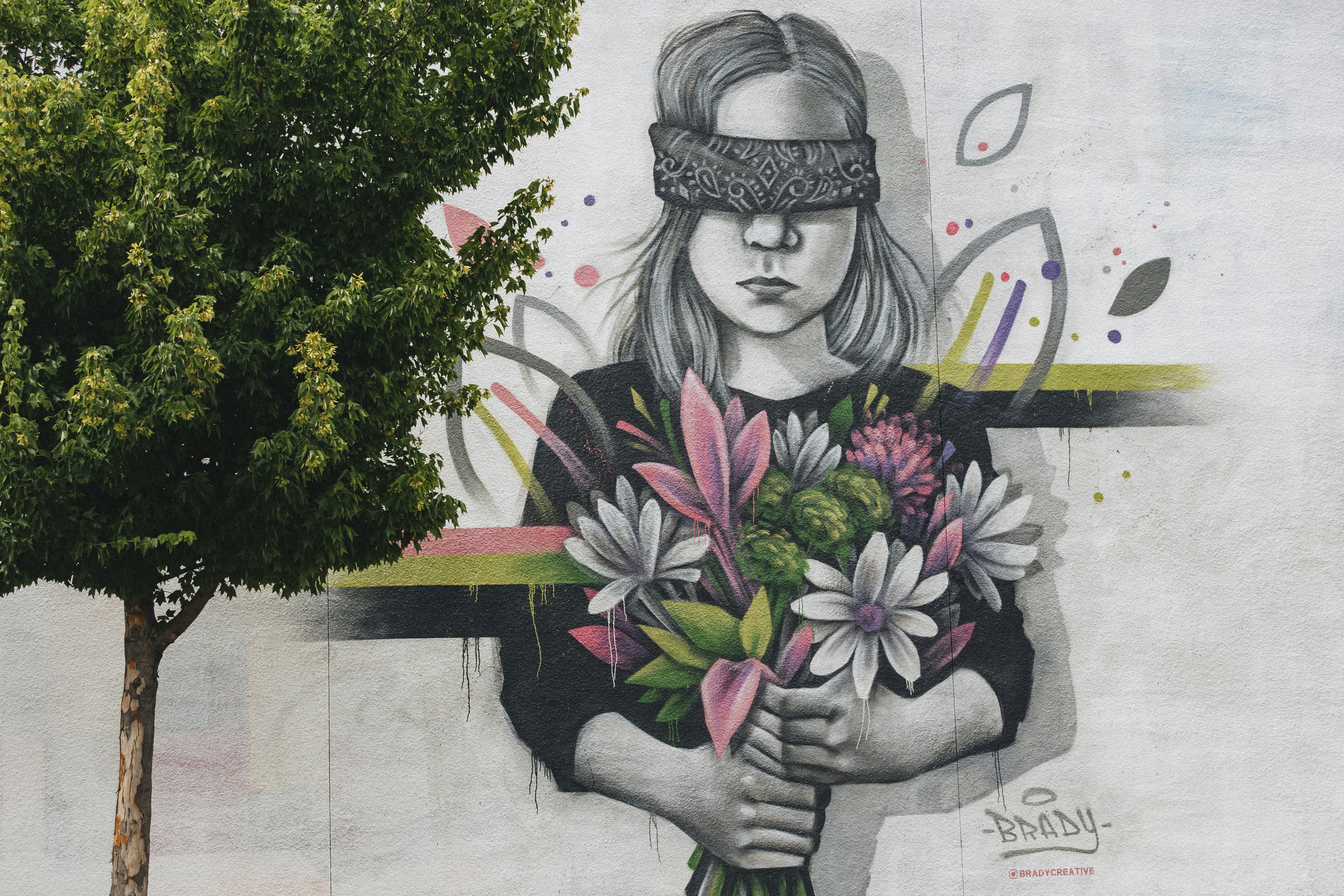 Mural of a girl with a blindfold holding a bouquet of flowers, set against a colorful background. The artwork conveys themes of perception and beauty.