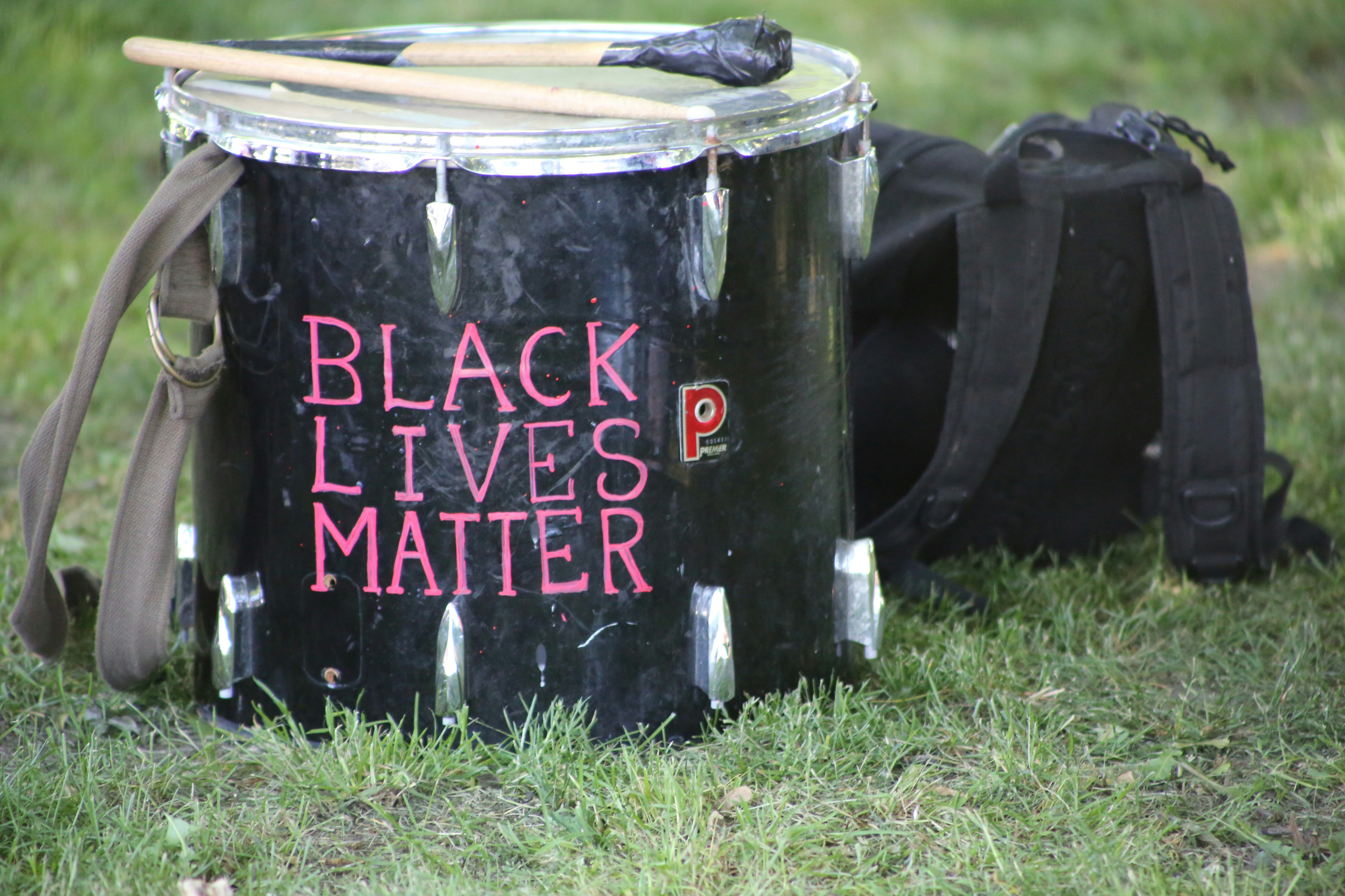 A drum adorned with the message 'BLACK LIVES MATTER' rests on the grass, accompanied by drumsticks and a bag, symbolizing the fusion of music and activism.