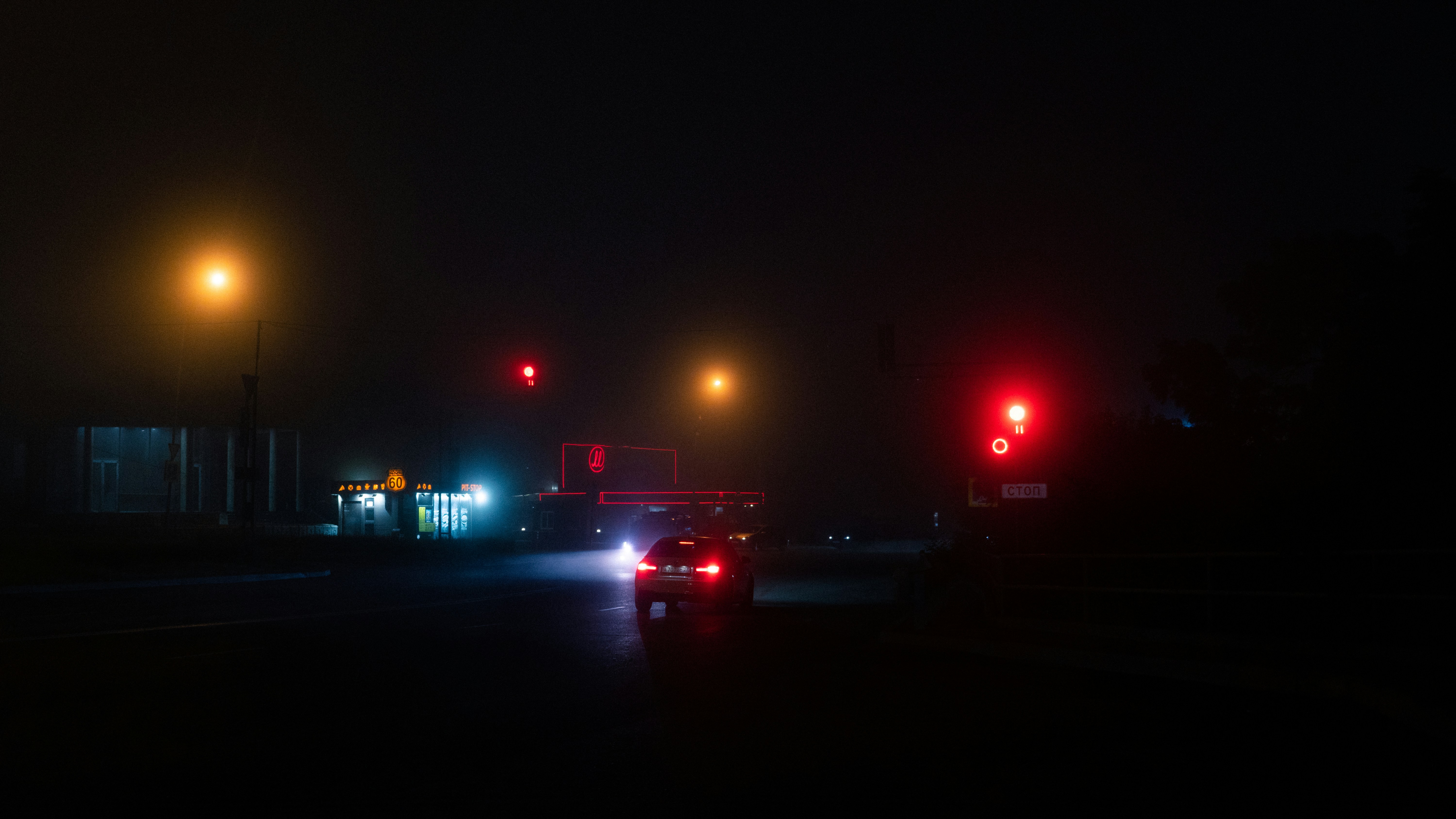 A solitary car navigates a foggy intersection, illuminated by streetlights and traffic signals. The scene captures the mysterious ambiance of a quiet urban night.