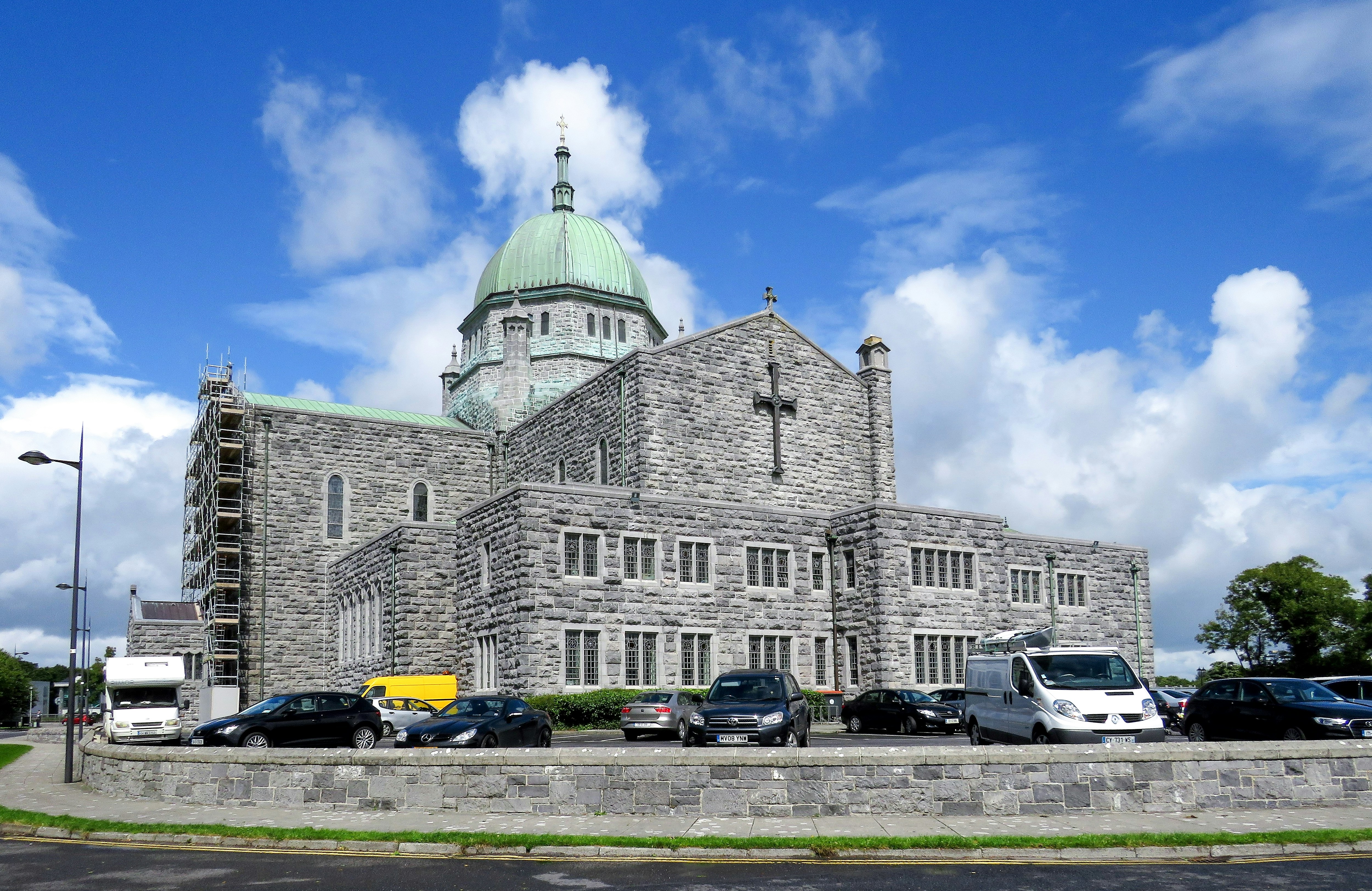 Granite cathedral with a large dome and cross, set against a backdrop of bright blue sky and clouds.