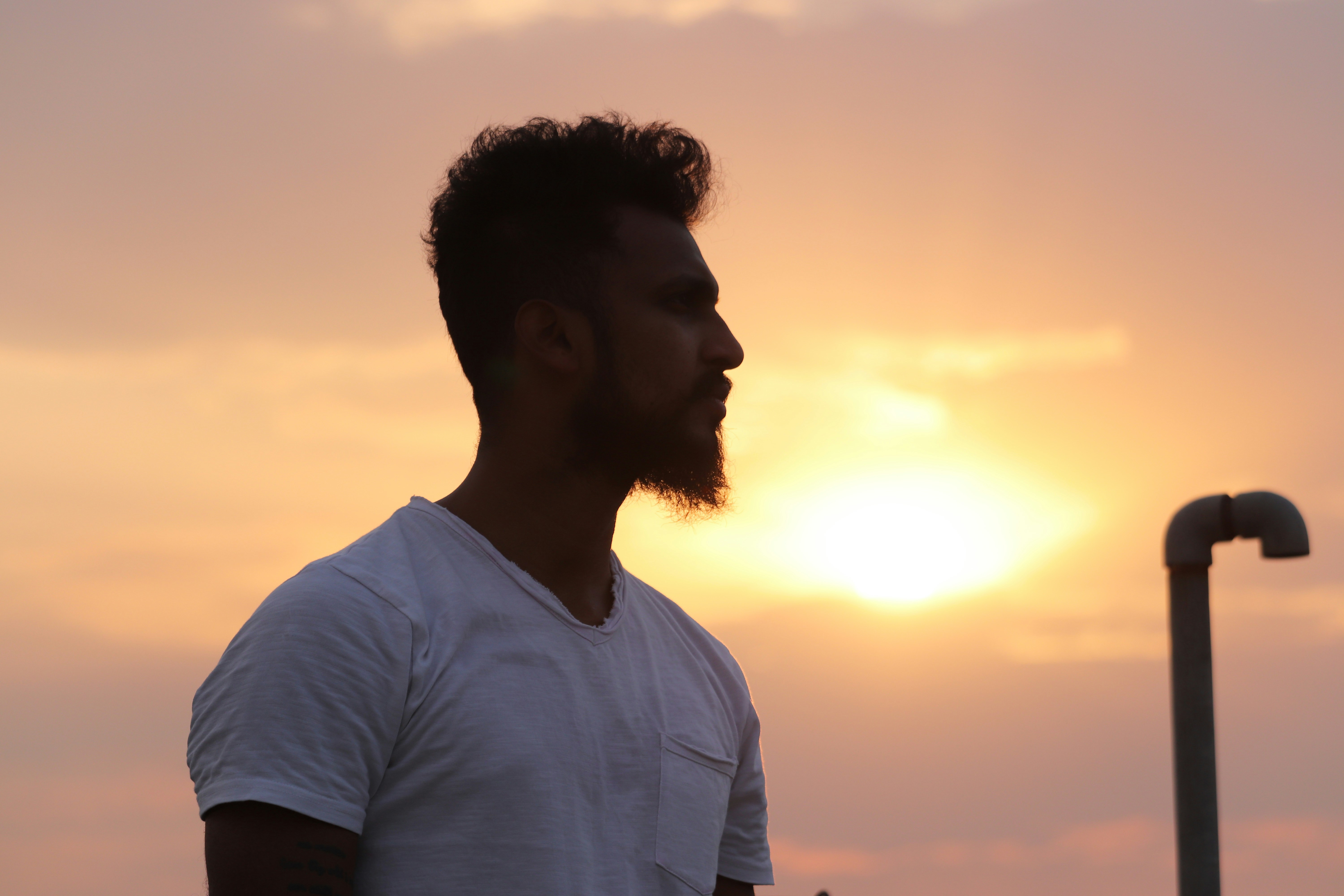 Silhouette of a man in a white shirt set against an orange-hued sunset sky.
