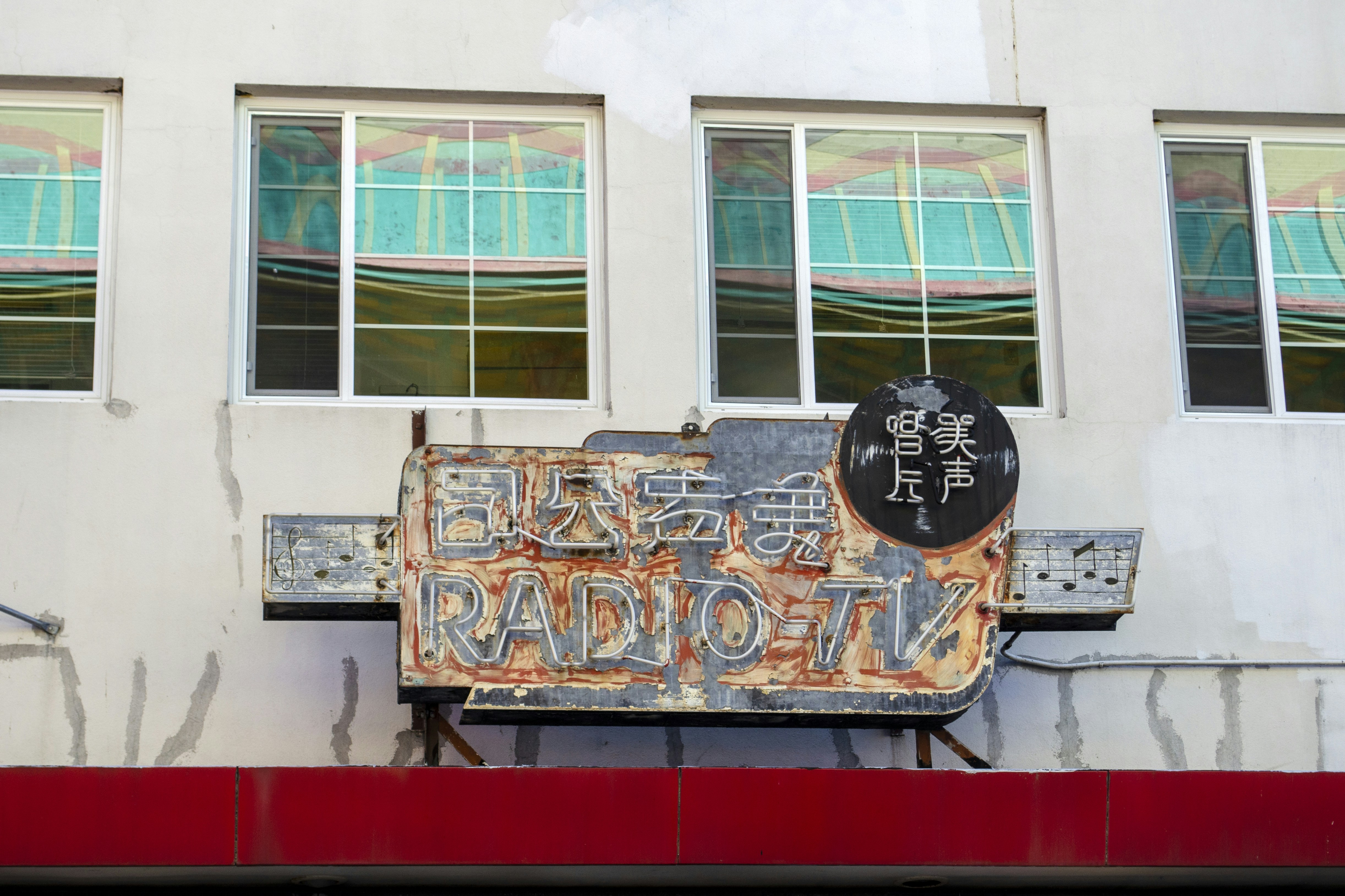 Rust and Neon Echo: The Weathered Radio-TV Sign Above a Red Storefront