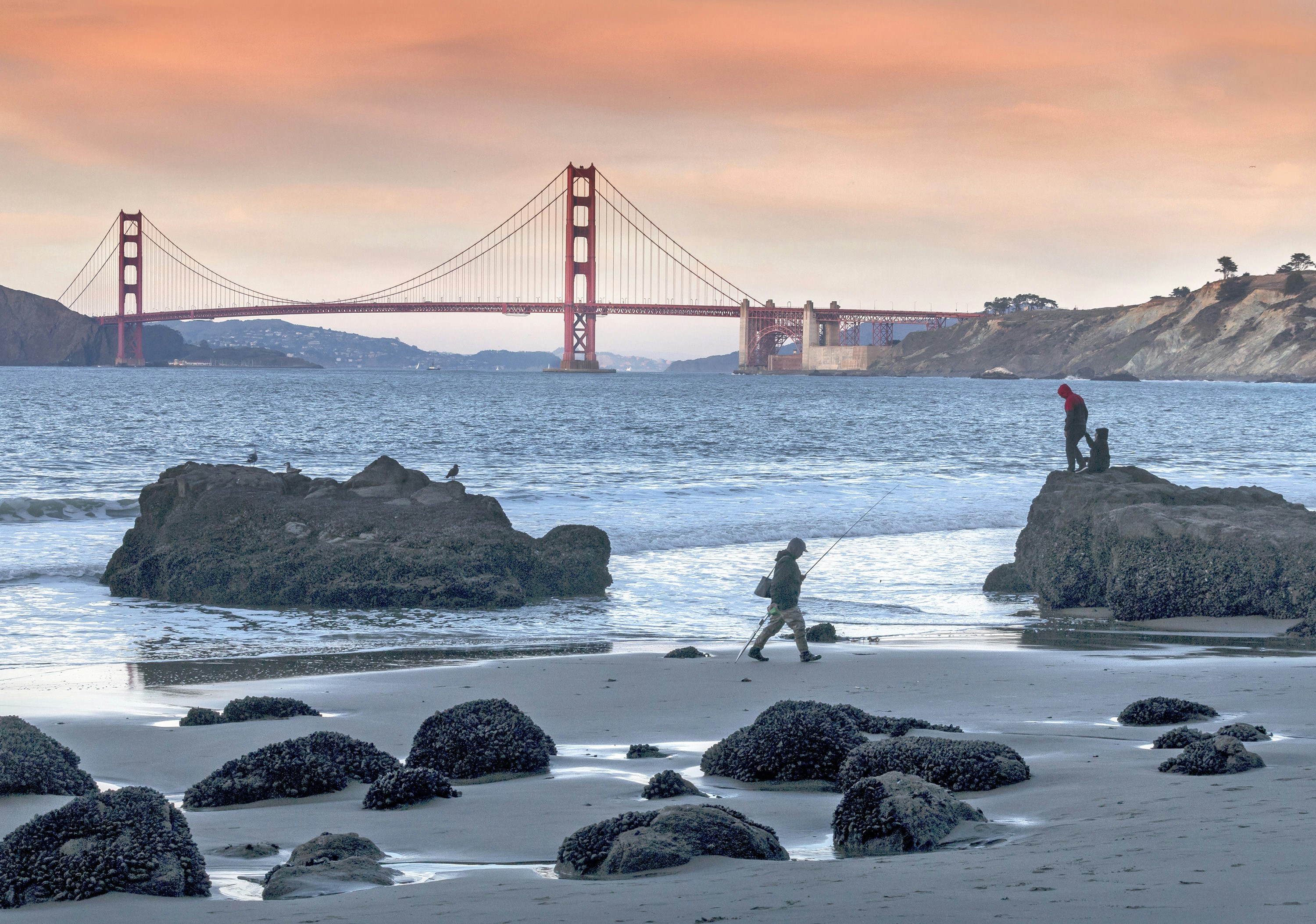Red-clad Silhouette on Tide-Washed Rocks Beneath the Golden Gate at Sunset