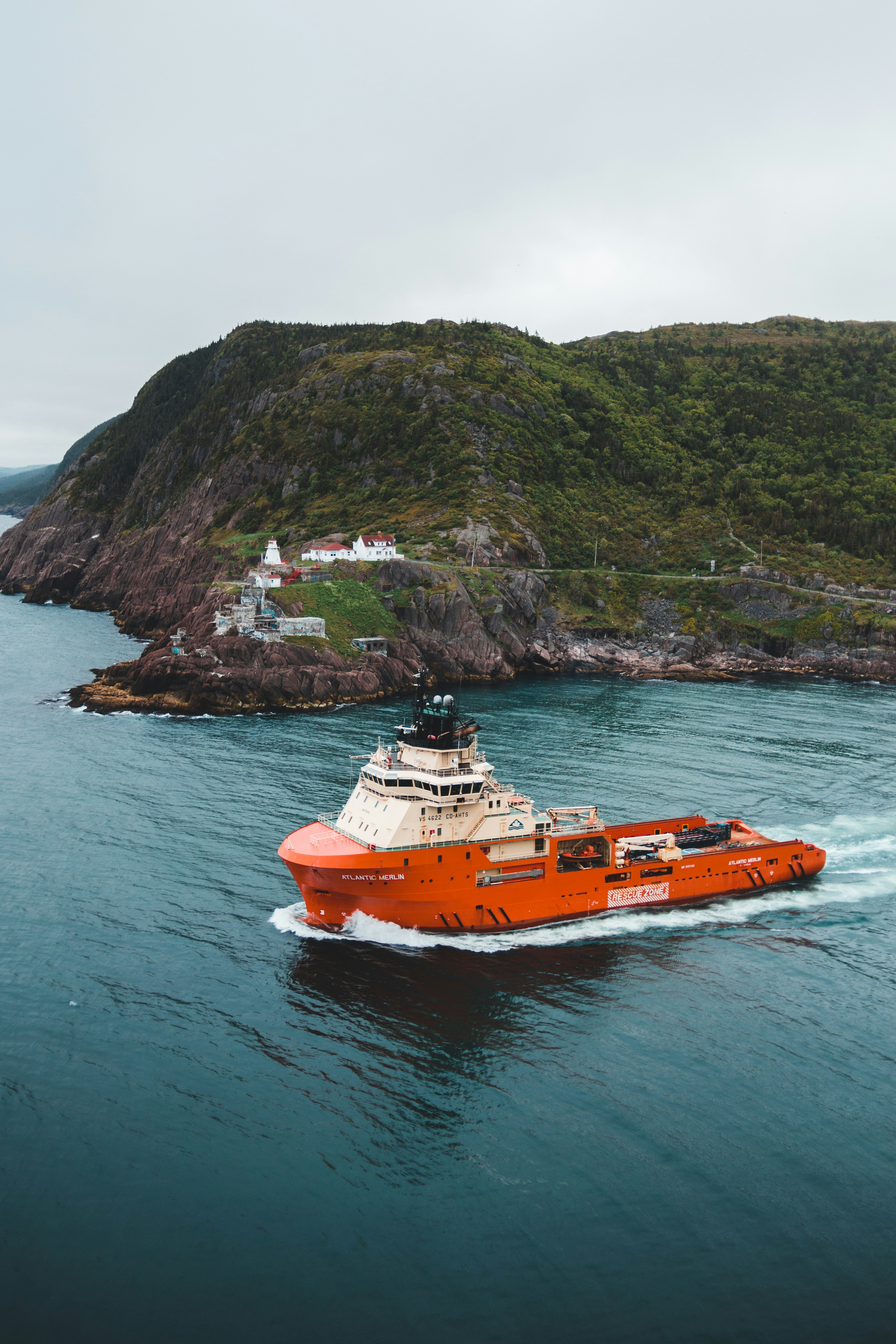 Orange Workboat Rounds the Rugged Cove Under Grey Skies
