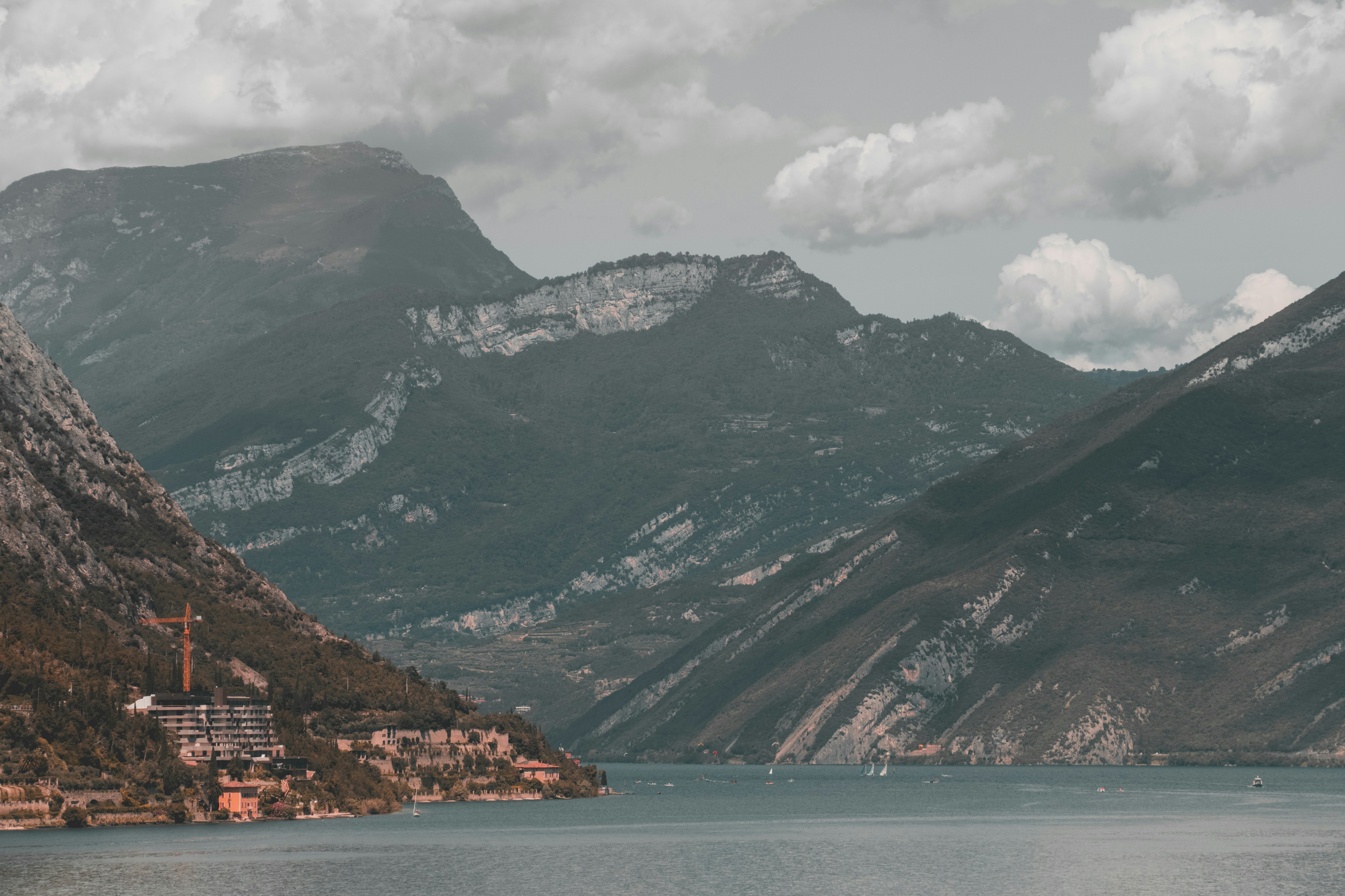 Tranquil lake bordered by steep, rugged mountains under a cloudy sky.