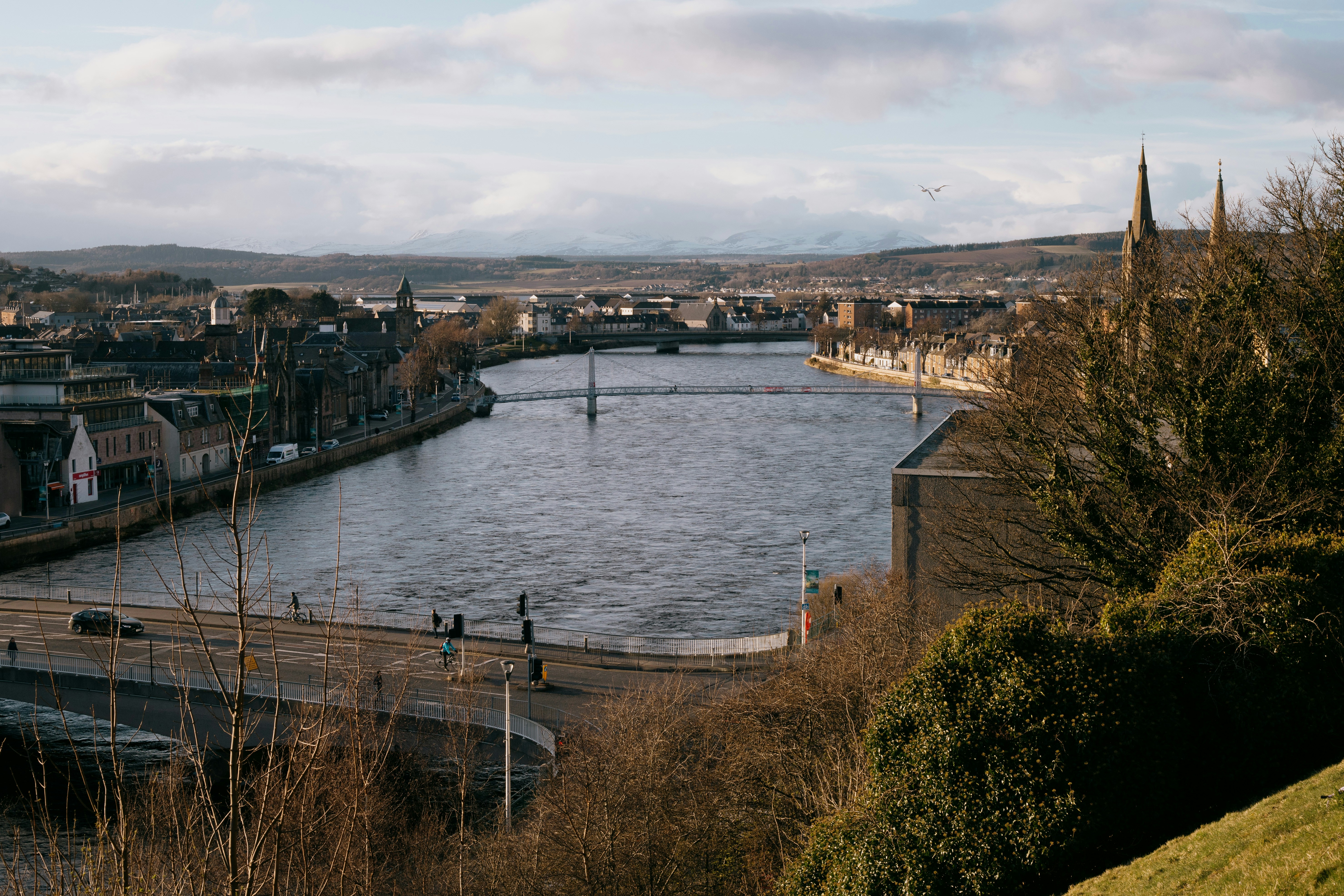 A tranquil view of a river winding through a city, showcasing bridges and historical architecture against a backdrop of rolling hills. The scene captures the essence of urban life harmonized with nature.