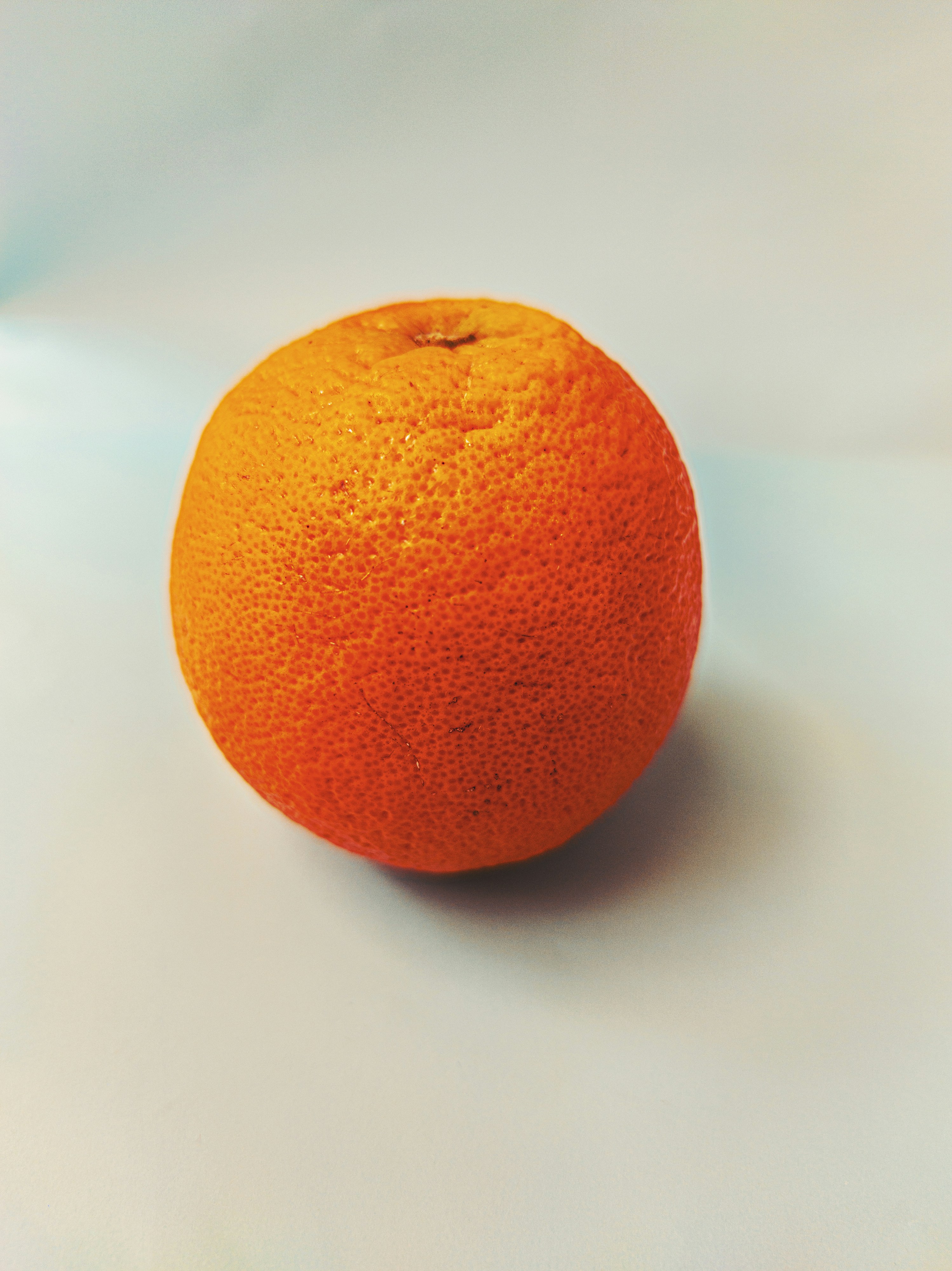 Vibrant orange fruit resting on a soft blue background, showcasing its textured skin and natural sheen.