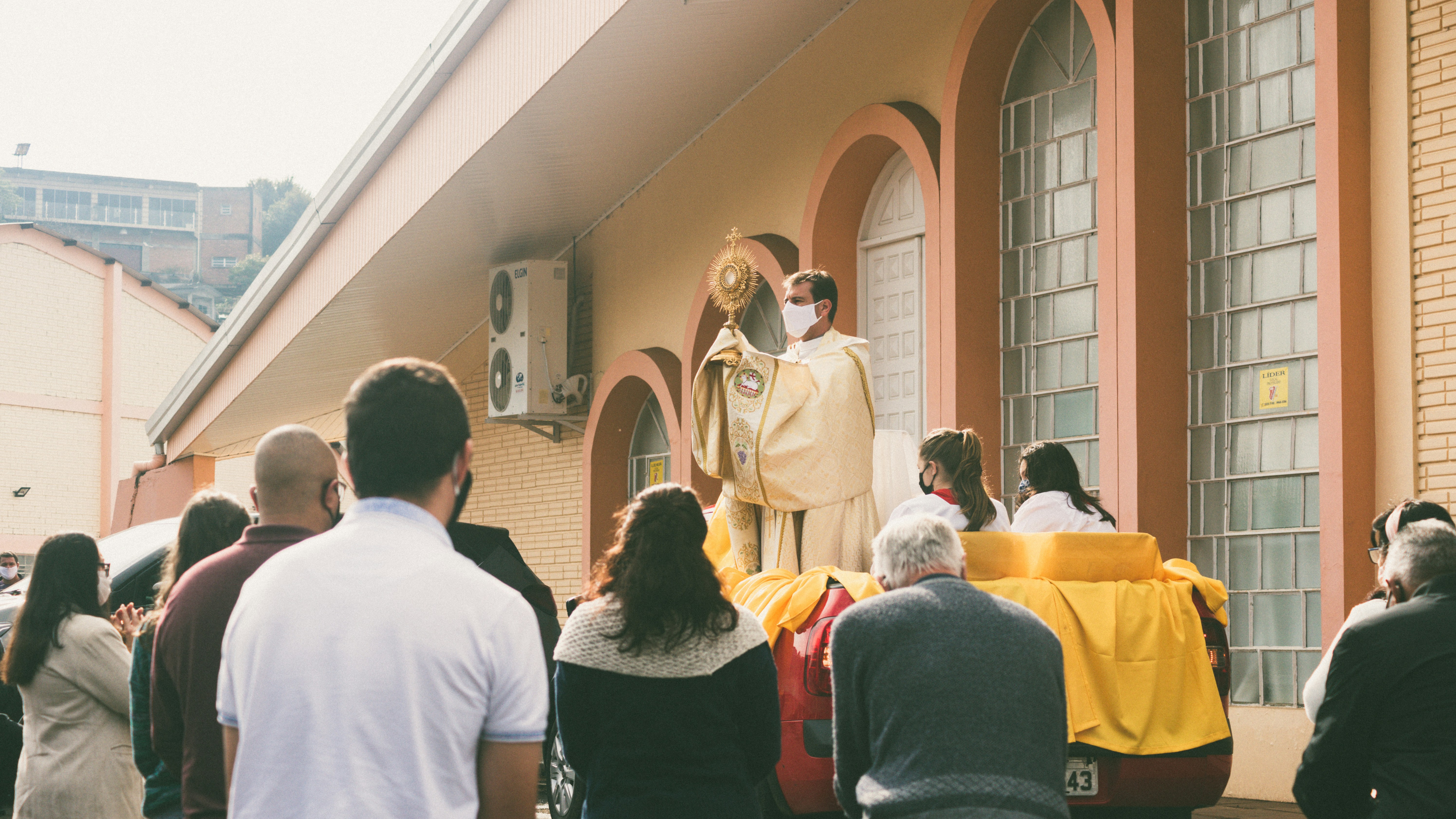 Group of people in white and yellow shirts standing before a building with arched windows during daylight.