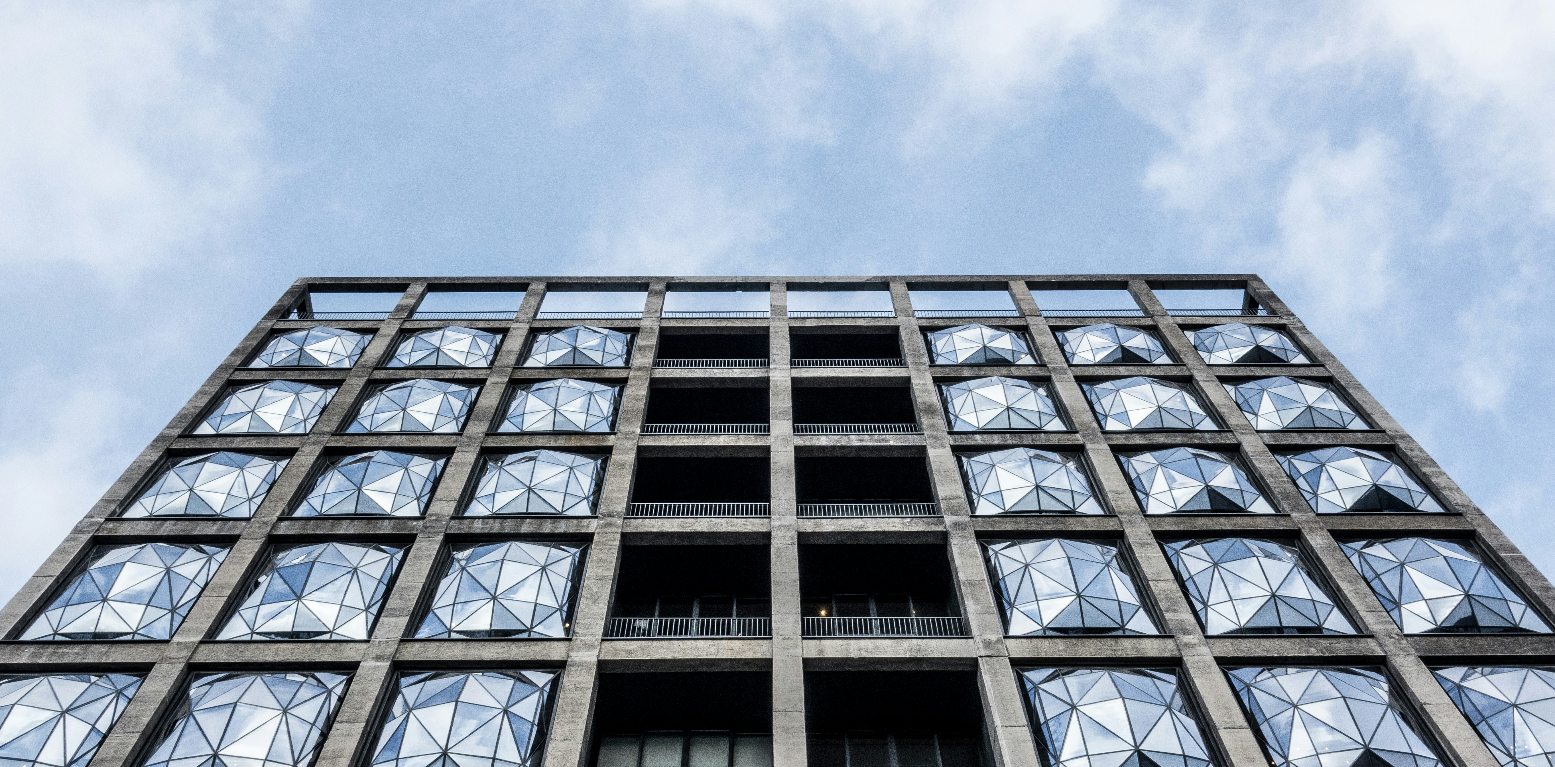 Modern building facade with geometric glass windows reflecting the sky.