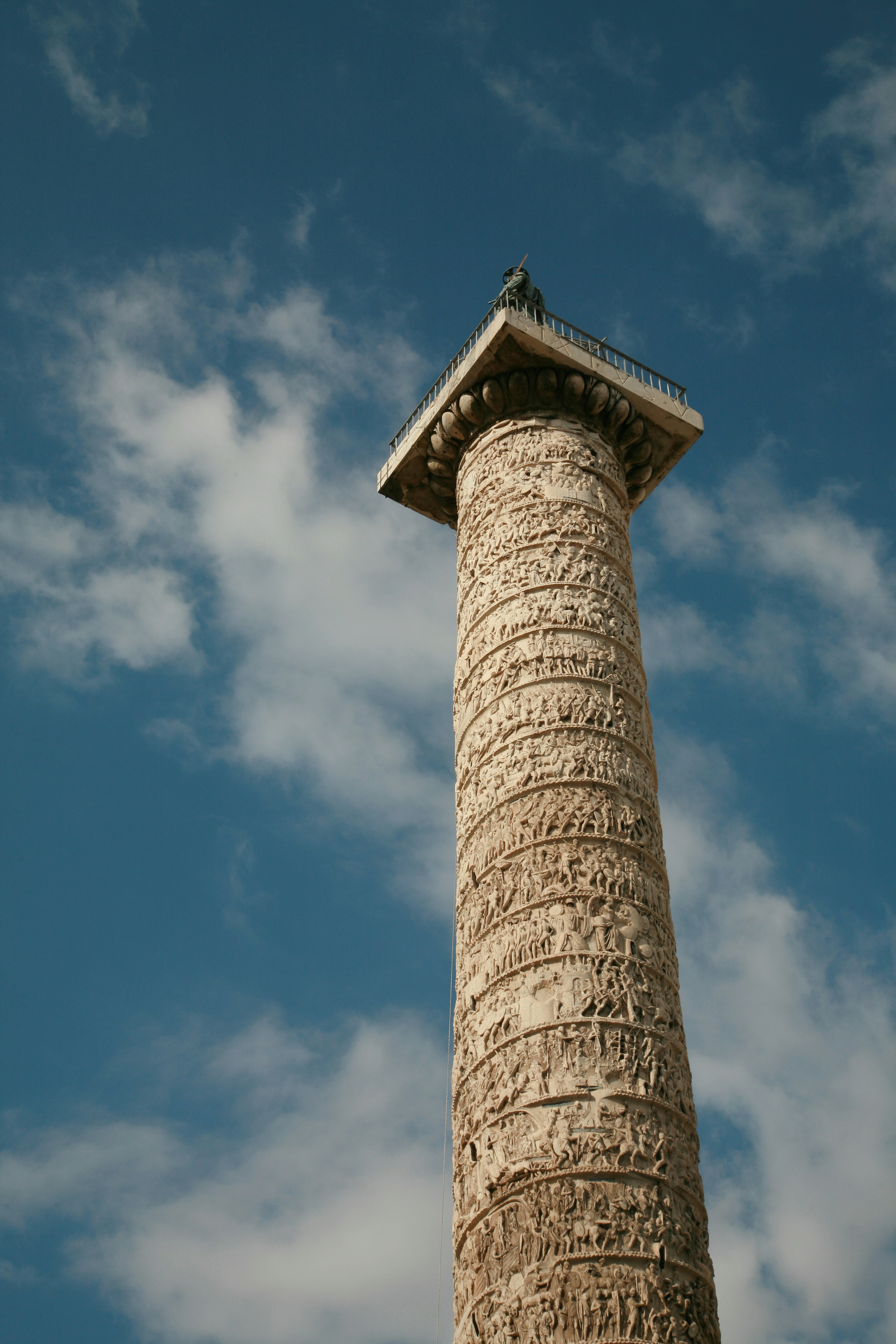 An intricately carved column rises towards a bright sky, showcasing detailed reliefs that narrate ancient tales. The structure stands as a testament to historical artistry.