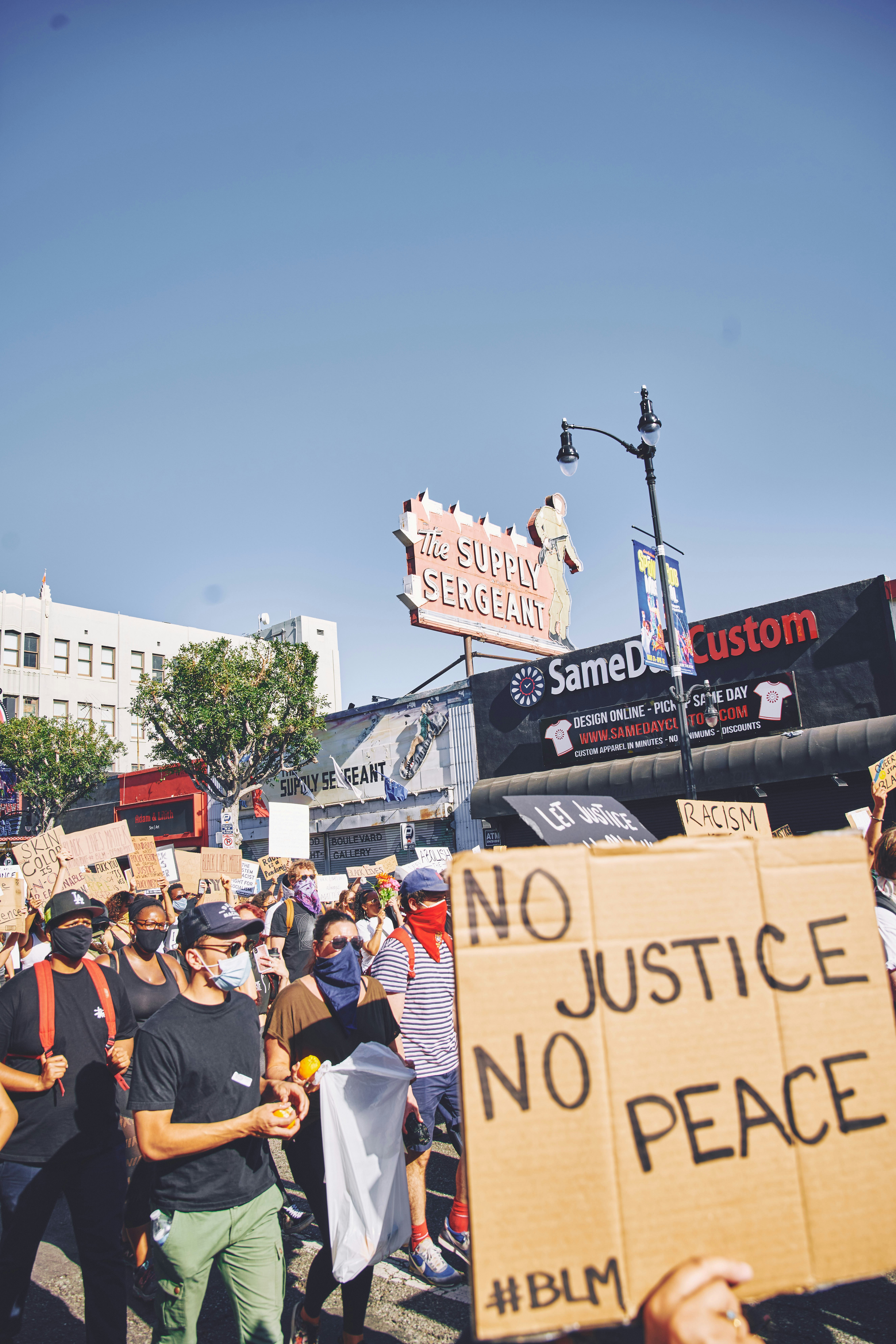 Sunlit Street Protest: Cardboard Signs and Masked Faces Demand Justice