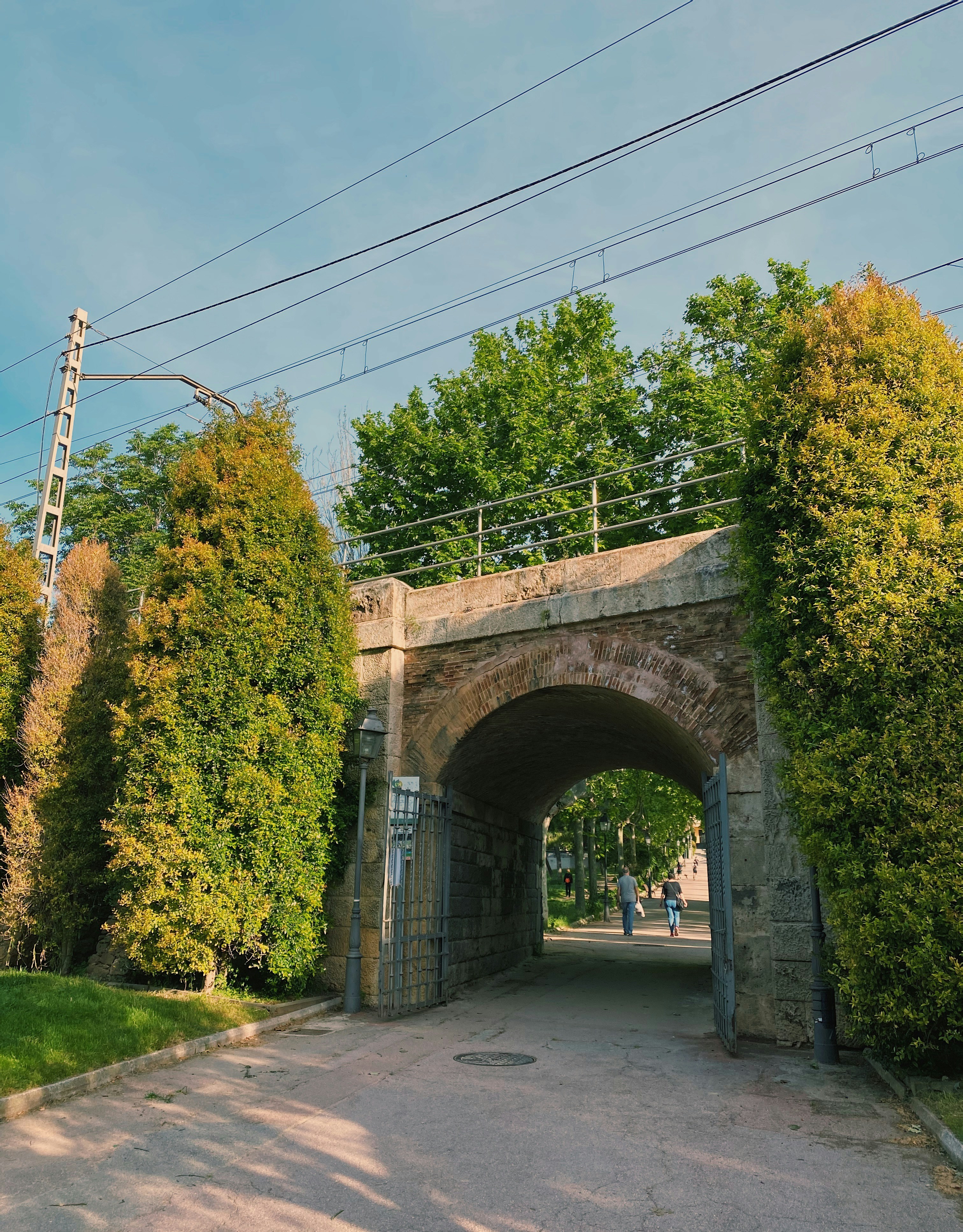 Archway surrounded by lush greenery leading to a tranquil path, inviting exploration. The scene captures a moment of leisure under a clear sky.