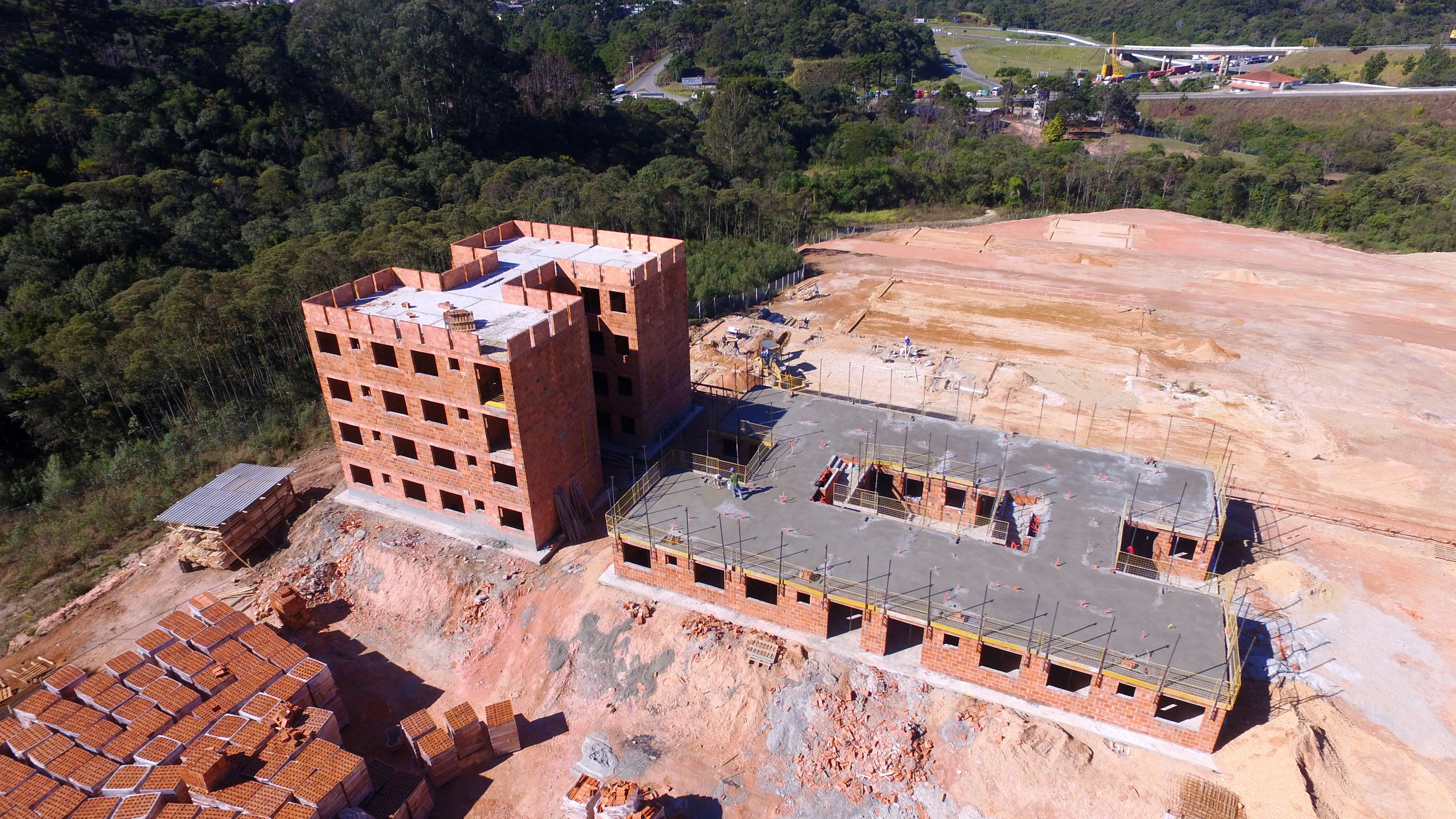 Drone view of a partially constructed residential building surrounded by forest and open land.