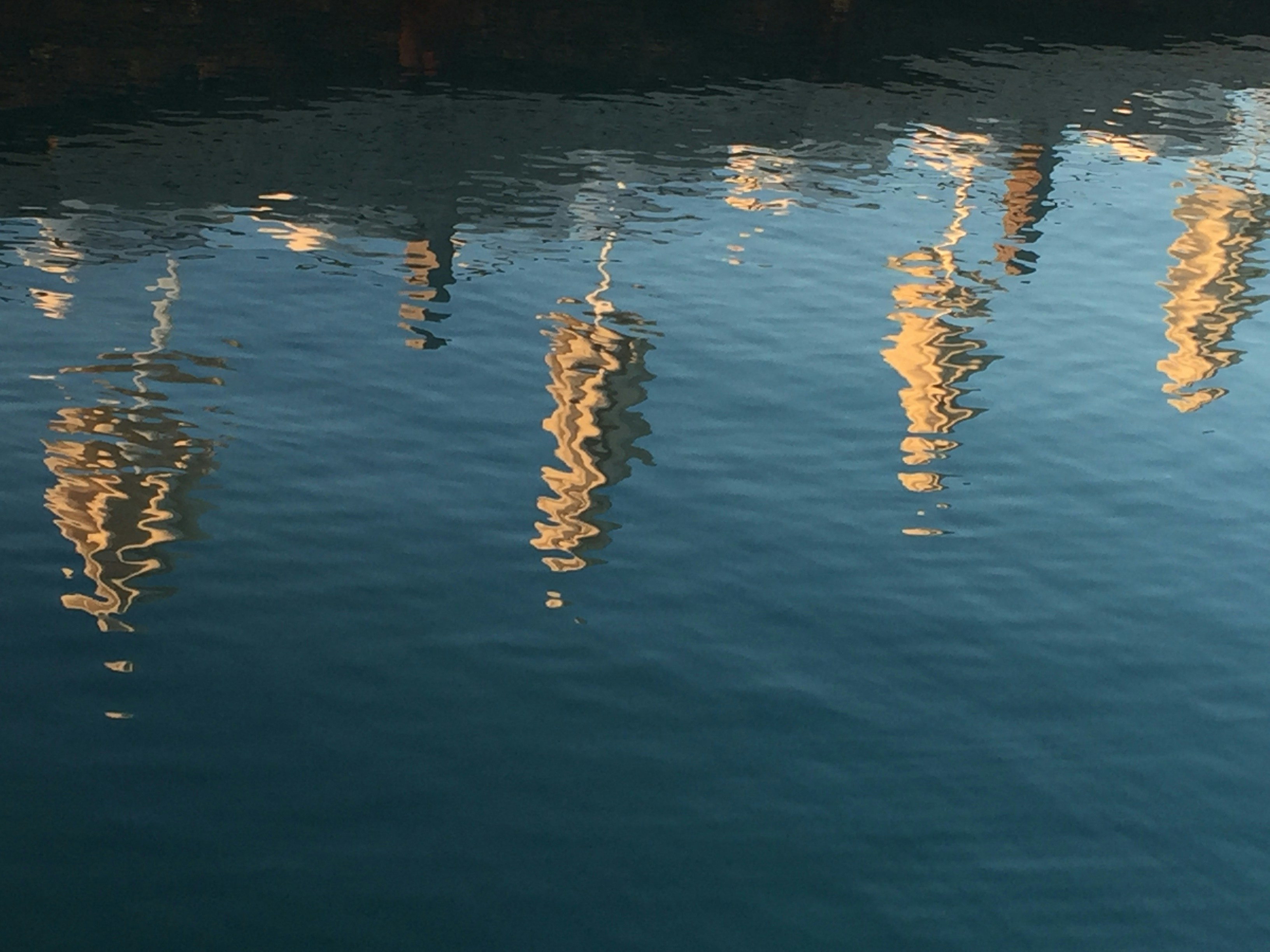 Golden reflections of structures ripple across a tranquil water surface, creating an abstract interplay of light and movement.