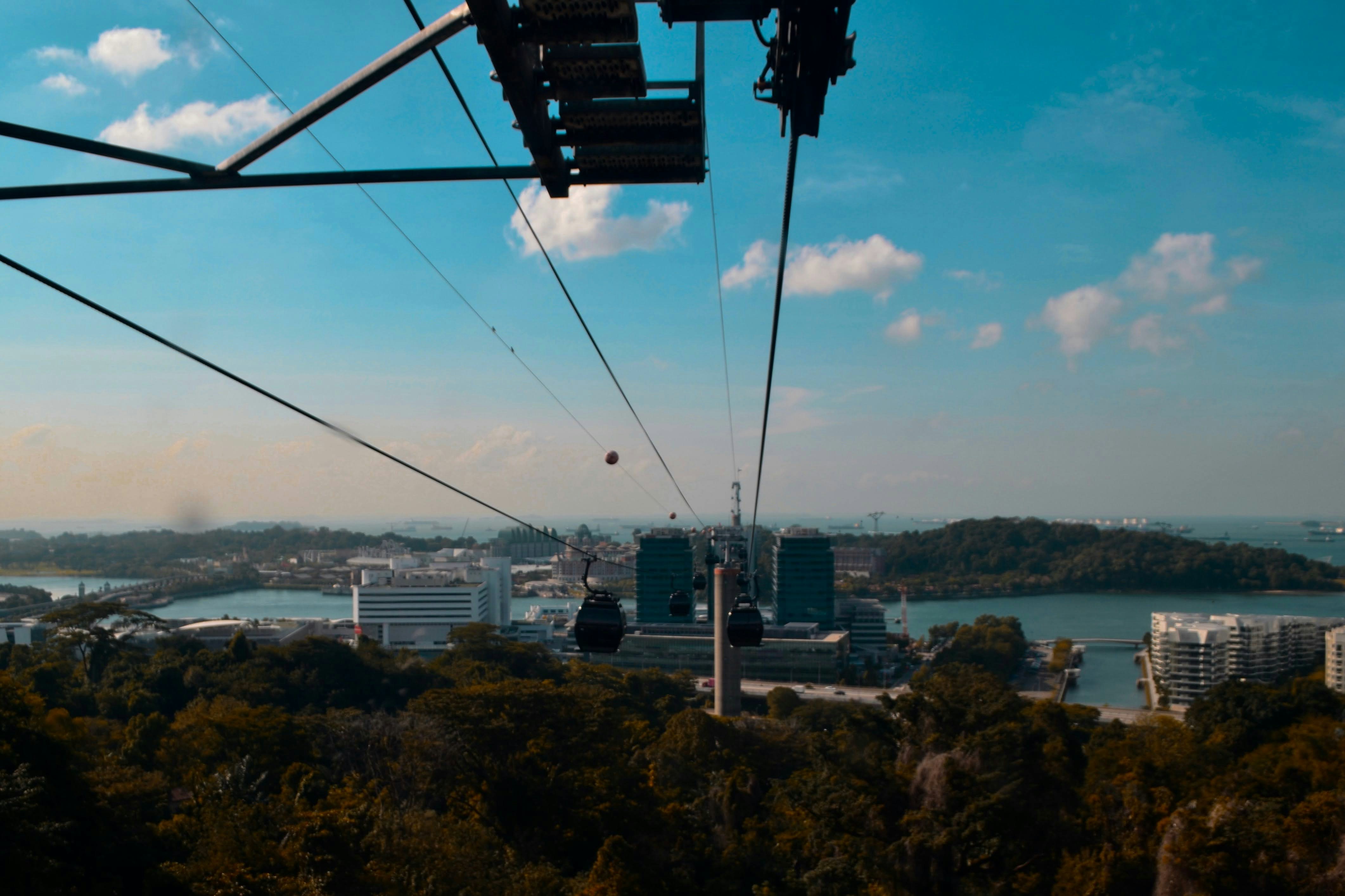 Cable cars gliding above a vibrant cityscape, framed by lush greenery and a serene bay. The scene captures the harmony between nature and urban life.