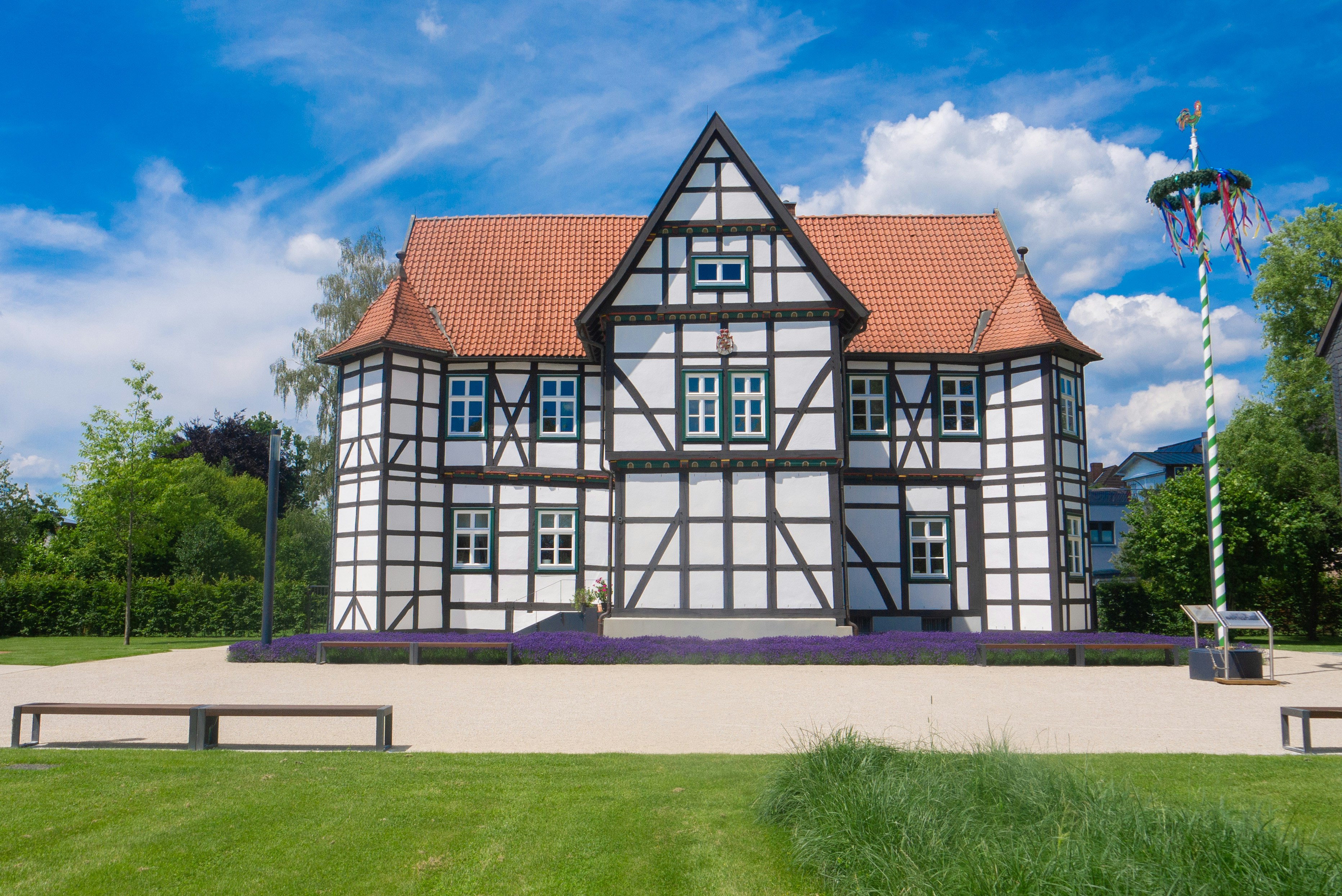 Traditional half-timbered house with a red roof set against a bright blue sky and lush greenery.