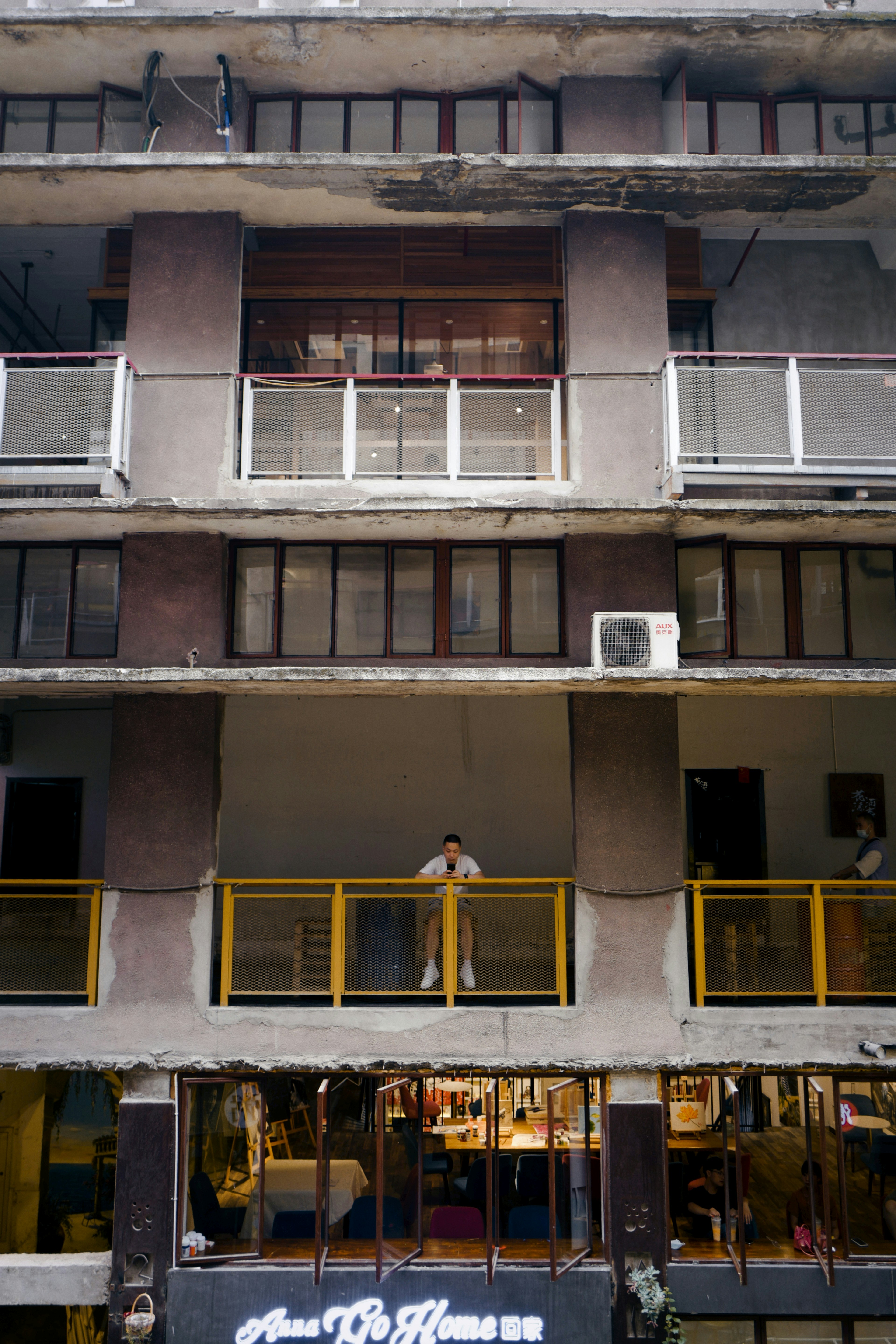 Midlevel Sentinel: A Quiet Figure Framed by Yellow Rails in a Weathered Atrium