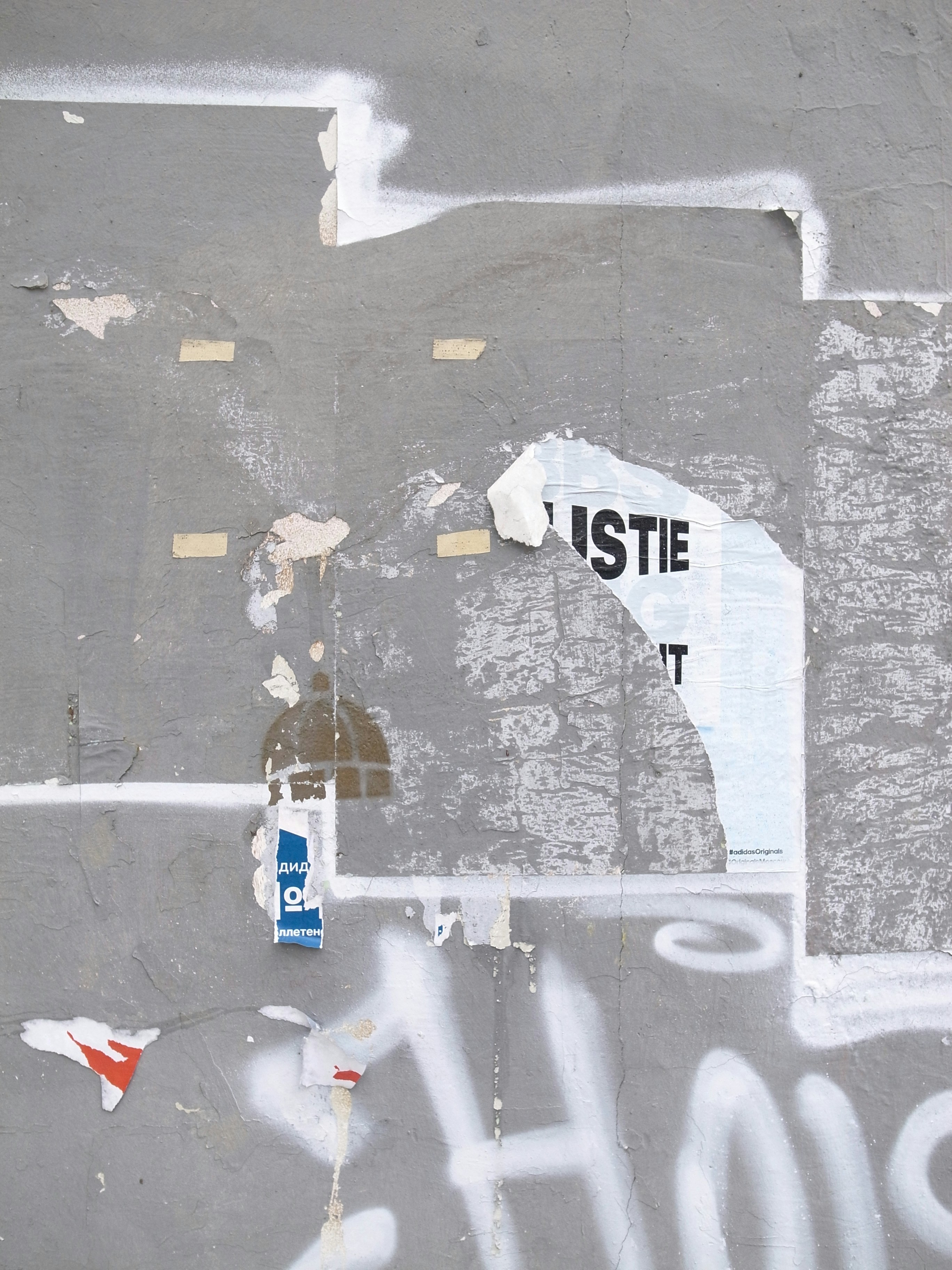 Peeling layers of paper and graffiti on a gray wall reveal a history of urban expression and neglect.