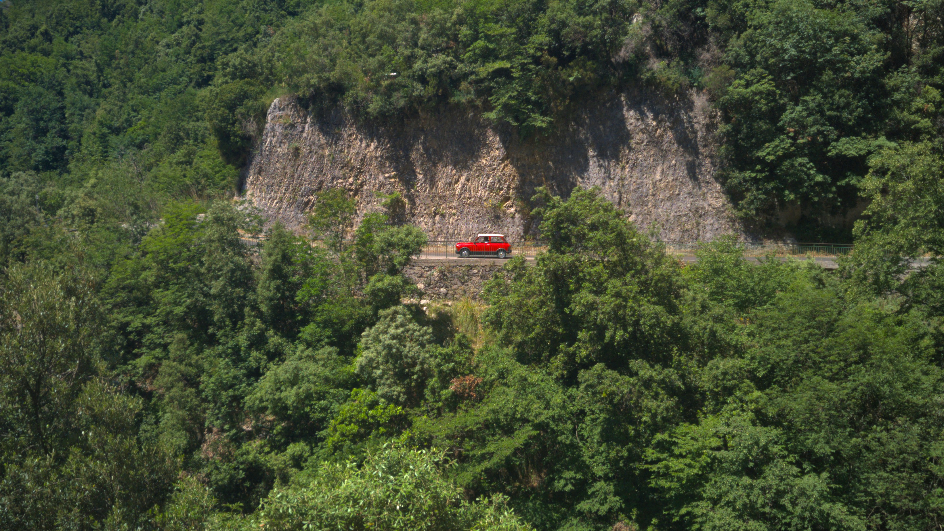 Crimson Car on a Cliffside Ribbon Through Emerald Pines
