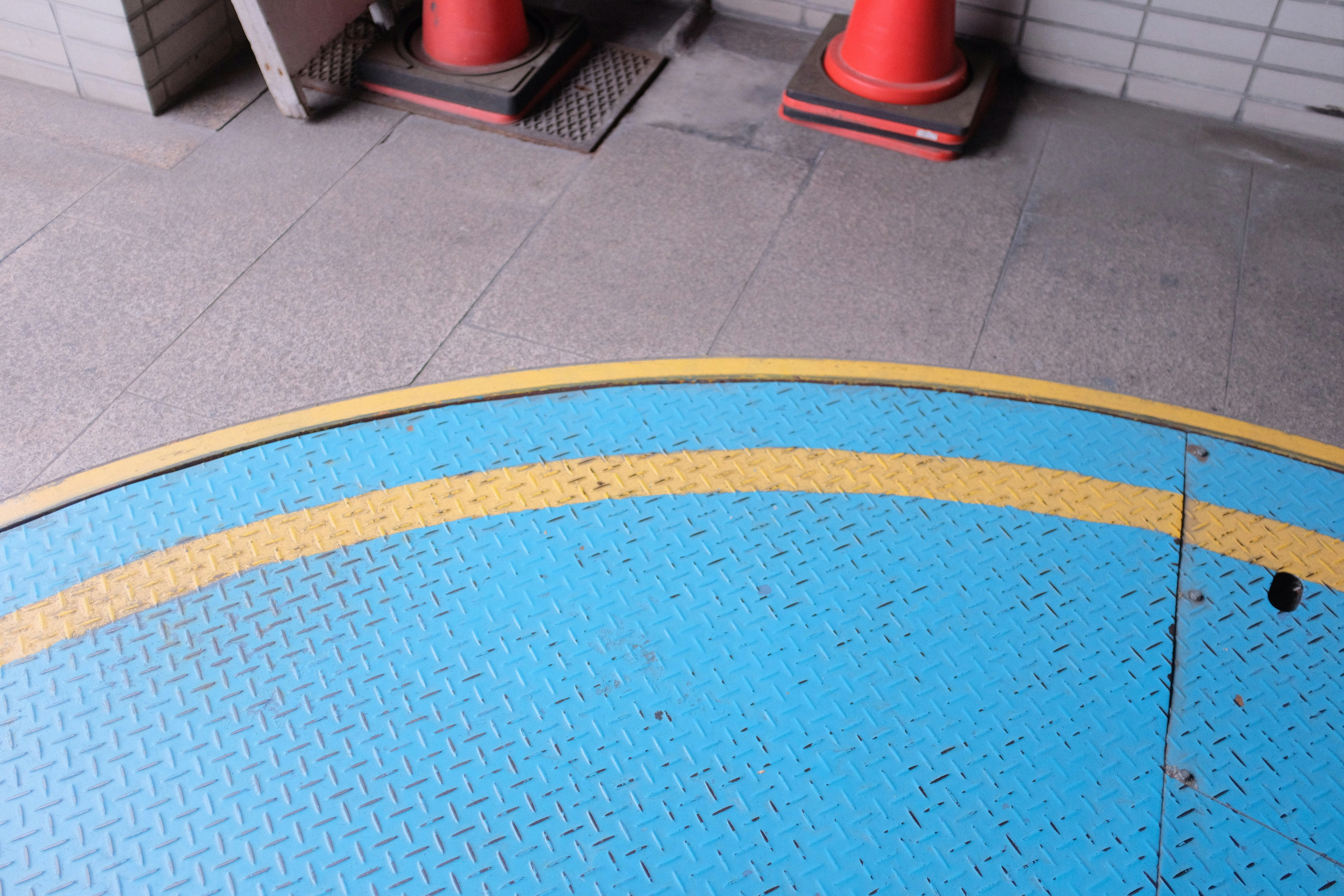 Vibrant blue circular surface with a yellow line, surrounded by safety cones in an urban setting.