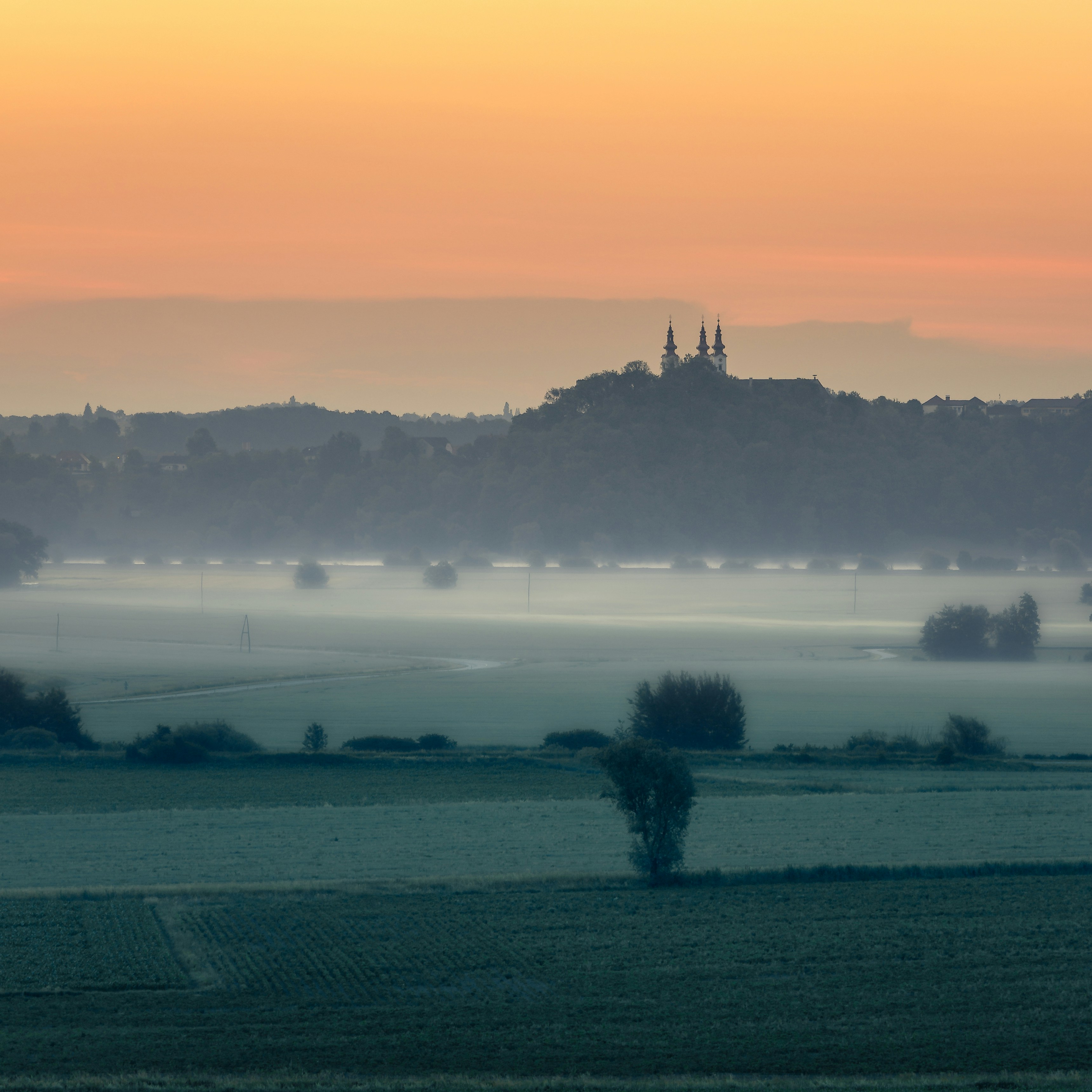 Pastel Horizon: Distant Church Silhouette Over Misty Fields