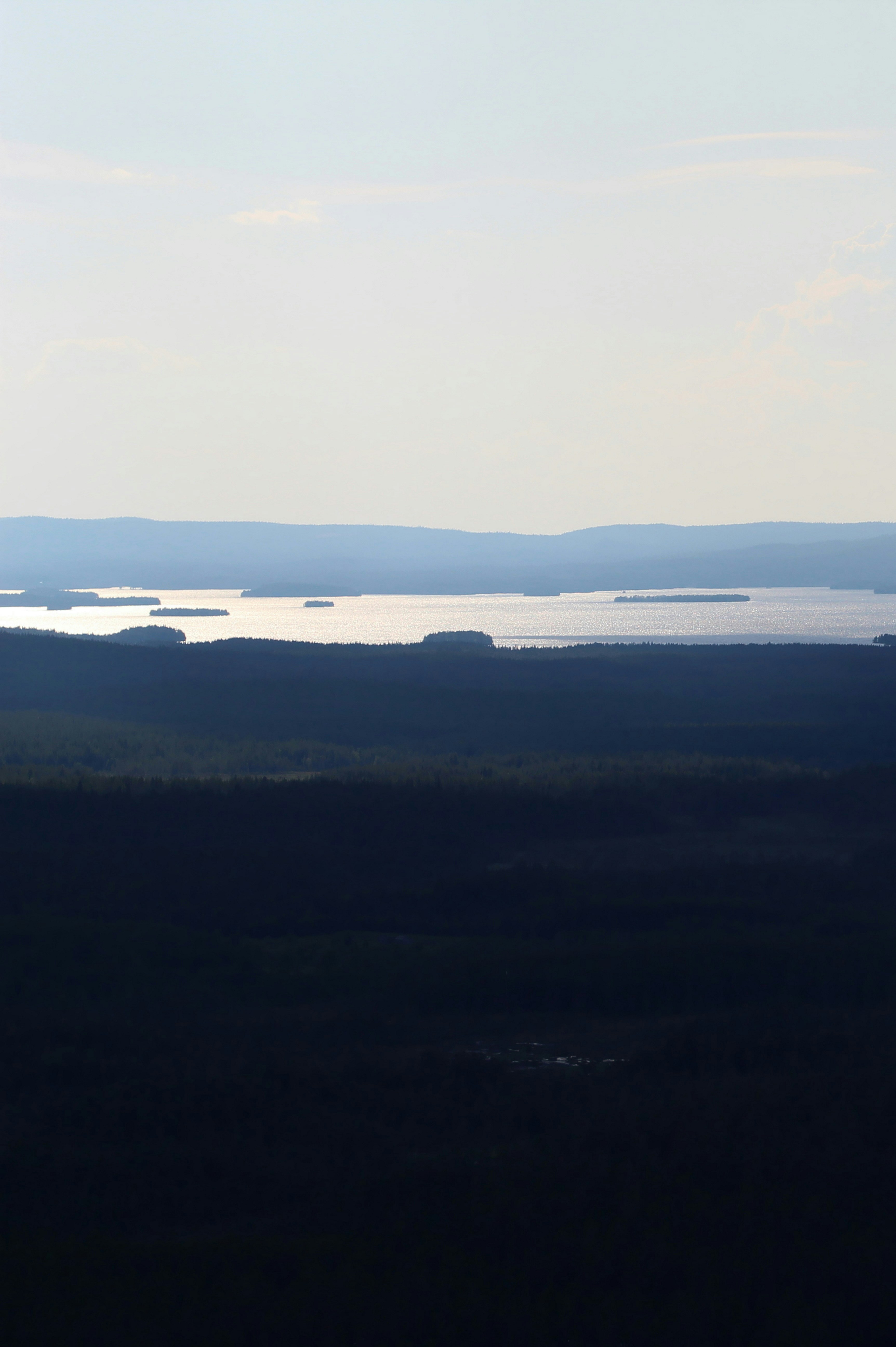 Serene view of a tranquil lake surrounded by distant hills under a soft sky. The shimmering water reflects the gentle light of the day.
