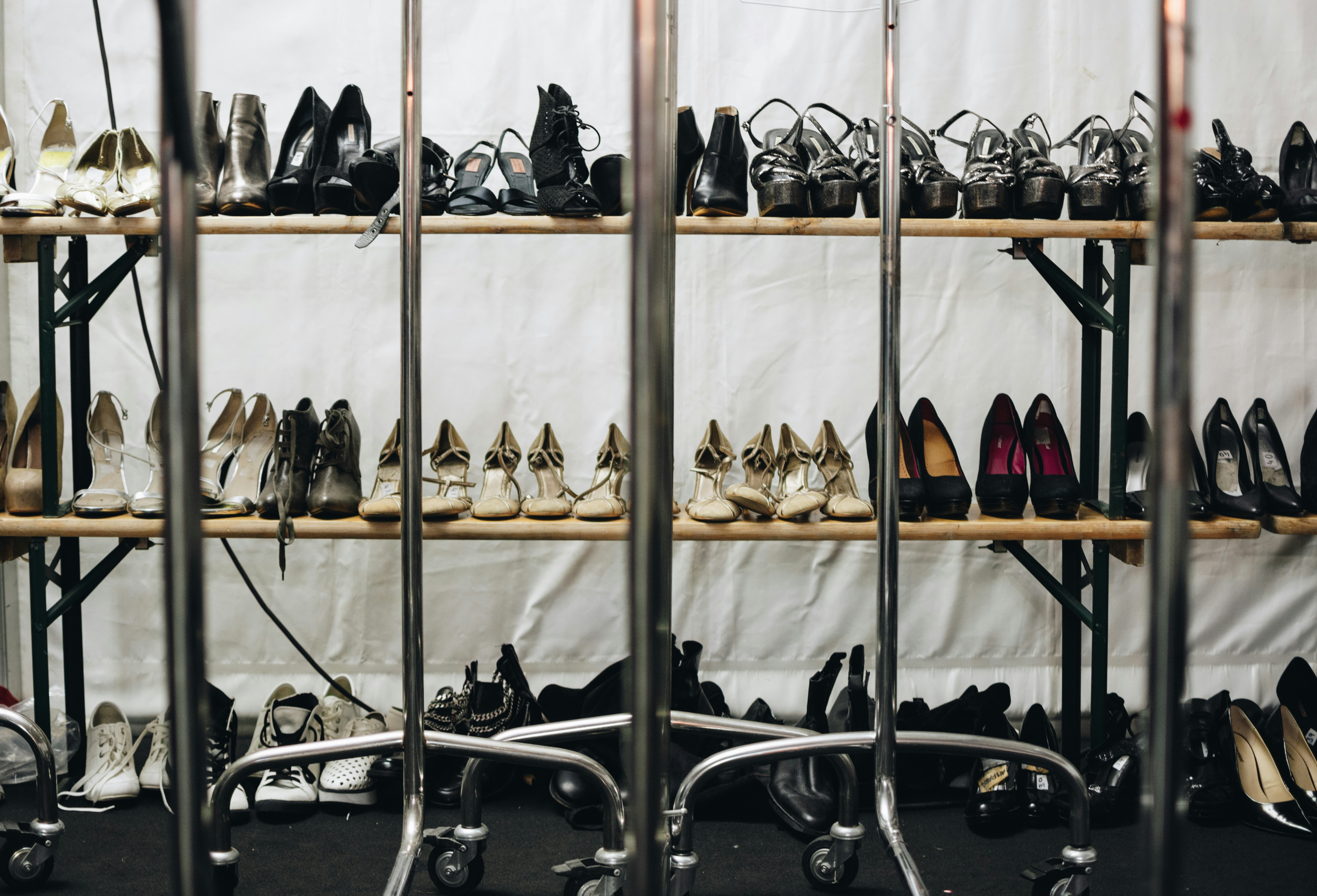 Arranged footwear on wooden shelves in a fashion setting, showcasing various styles and colors. The backdrop is a simple white fabric, enhancing the focus on the shoes.