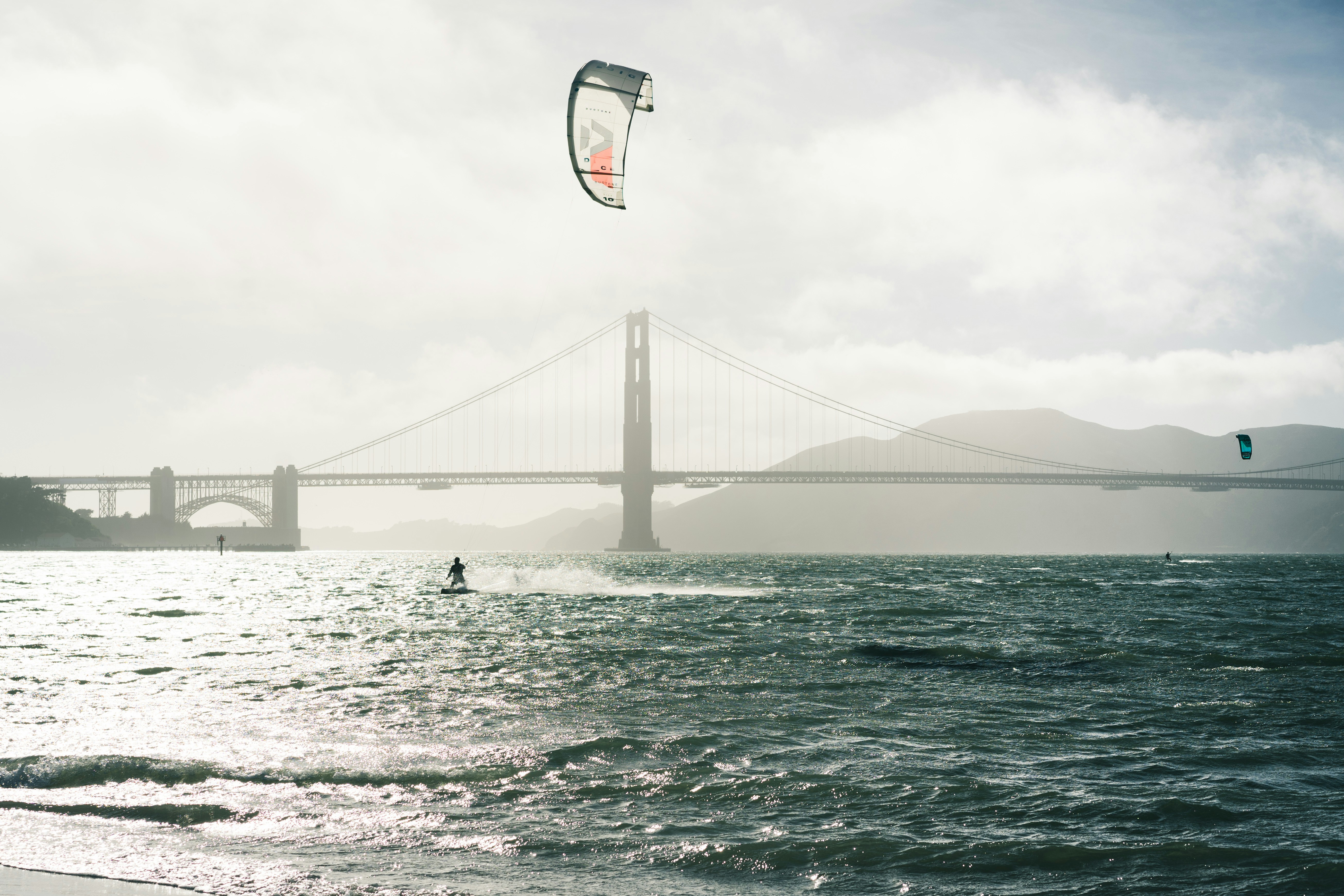 person surfing on sea near bridge under cloudy sky during daytime