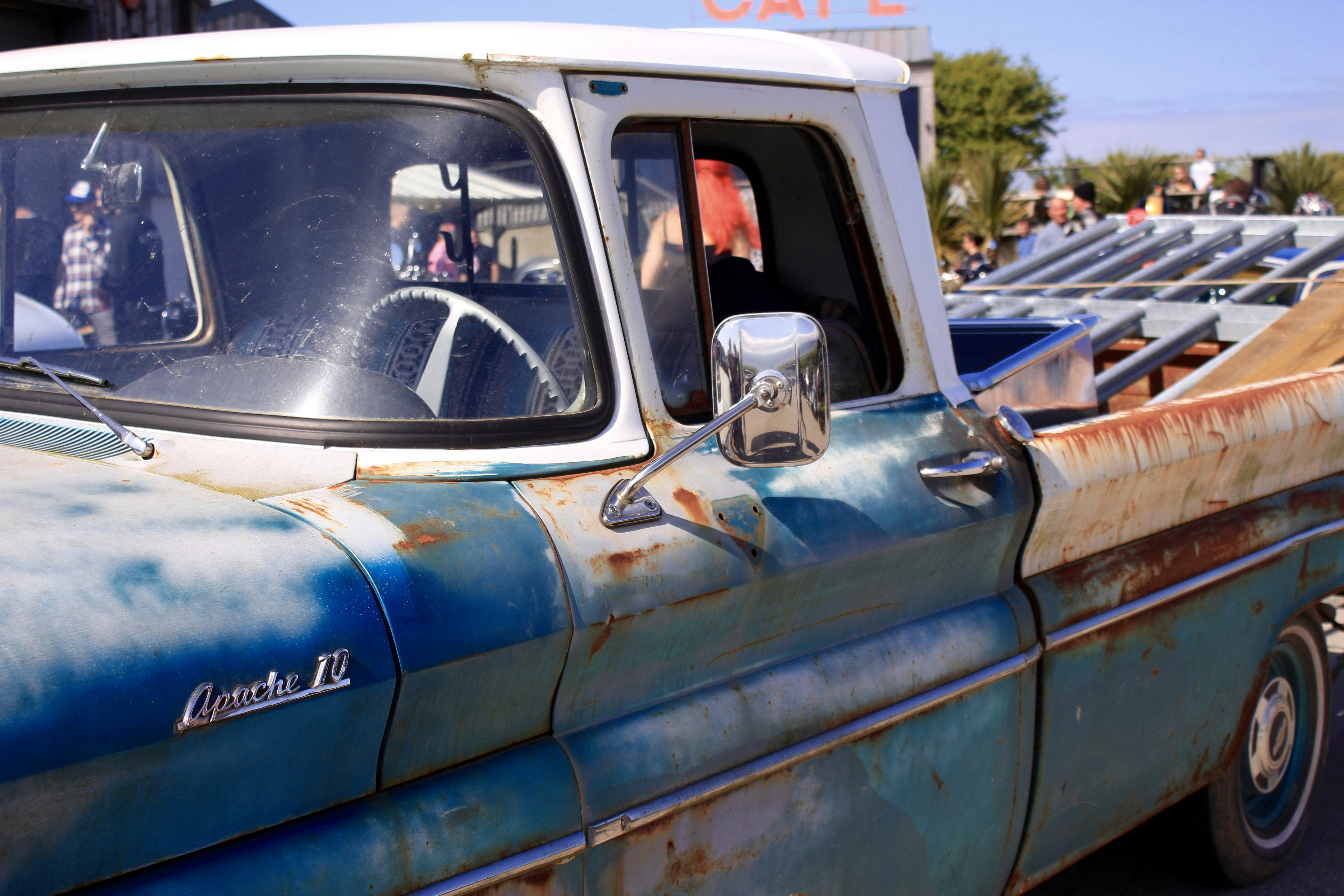 Close-up of a vintage Apache truck showcasing its weathered paint and classic design elements, with reflections in the chrome mirror. 