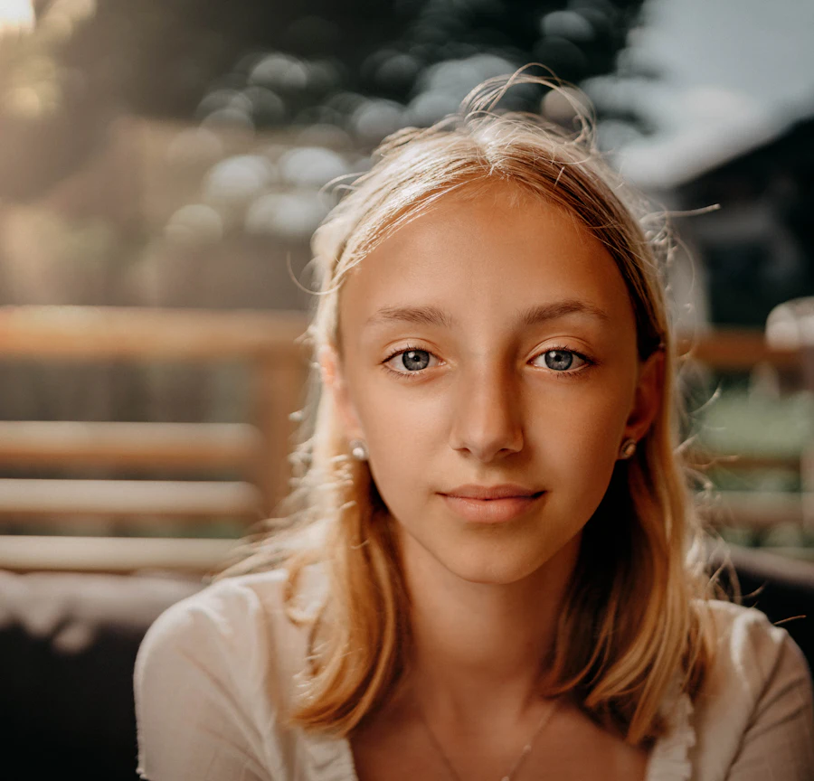 Young girl gazing thoughtfully with soft natural light illuminating her features. Background elements create a serene atmosphere.