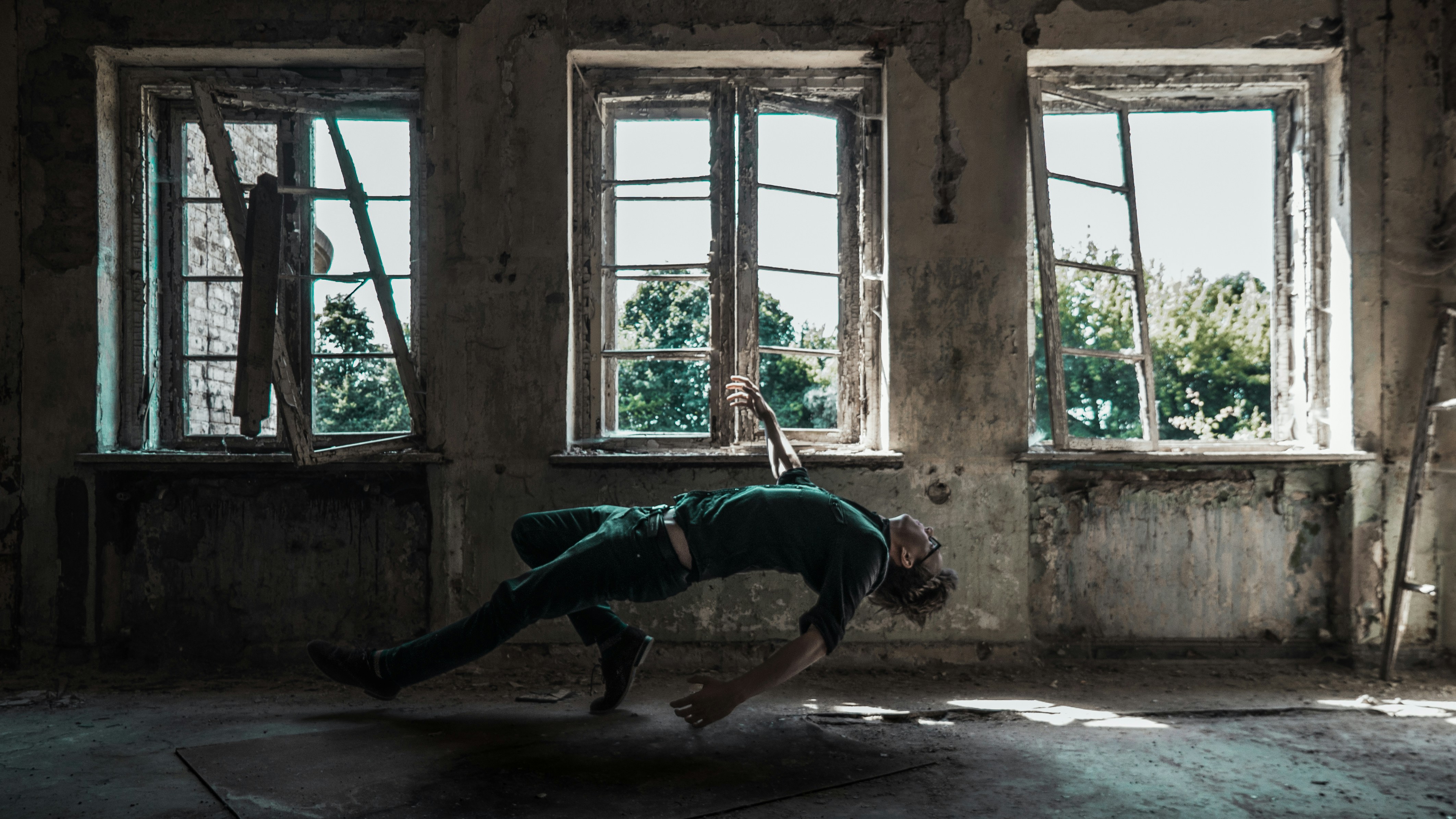 A dancer suspended in mid-air within a dilapidated room, surrounded by aged windows and natural light filtering through. The scene evokes a sense of surrealism and motion.