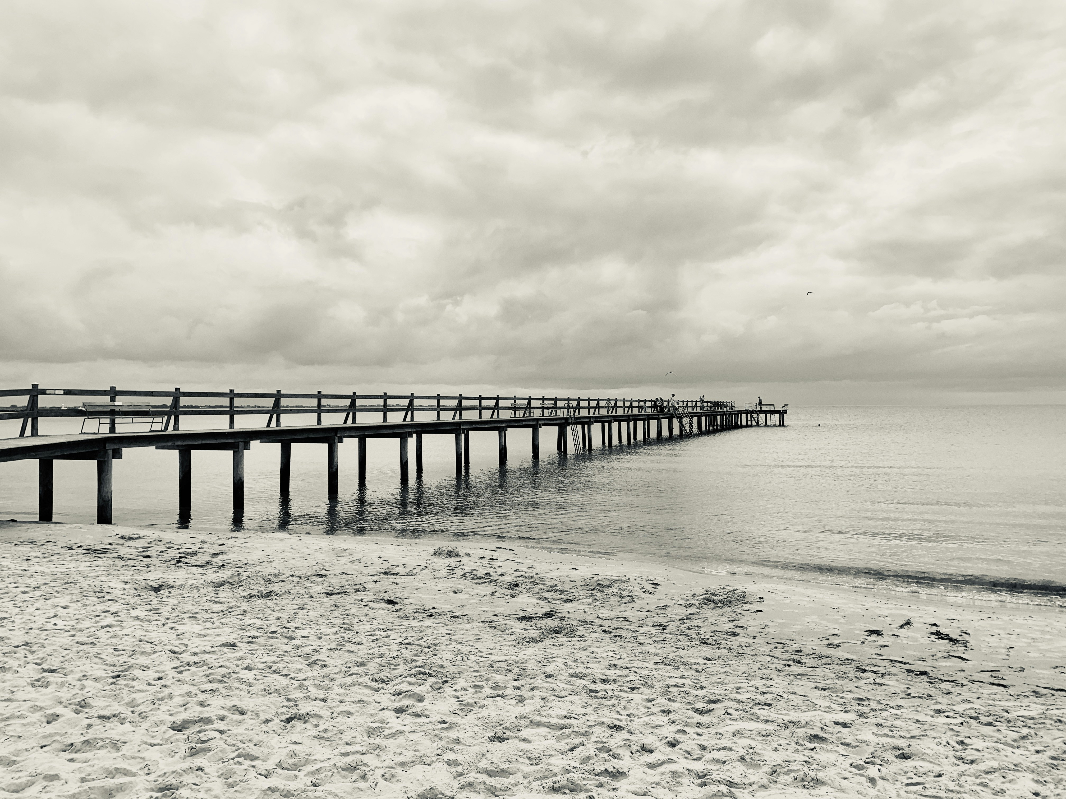 Weathered wooden pier extending into calm waters under a cloudy sky, evoking a sense of tranquility and reflection.