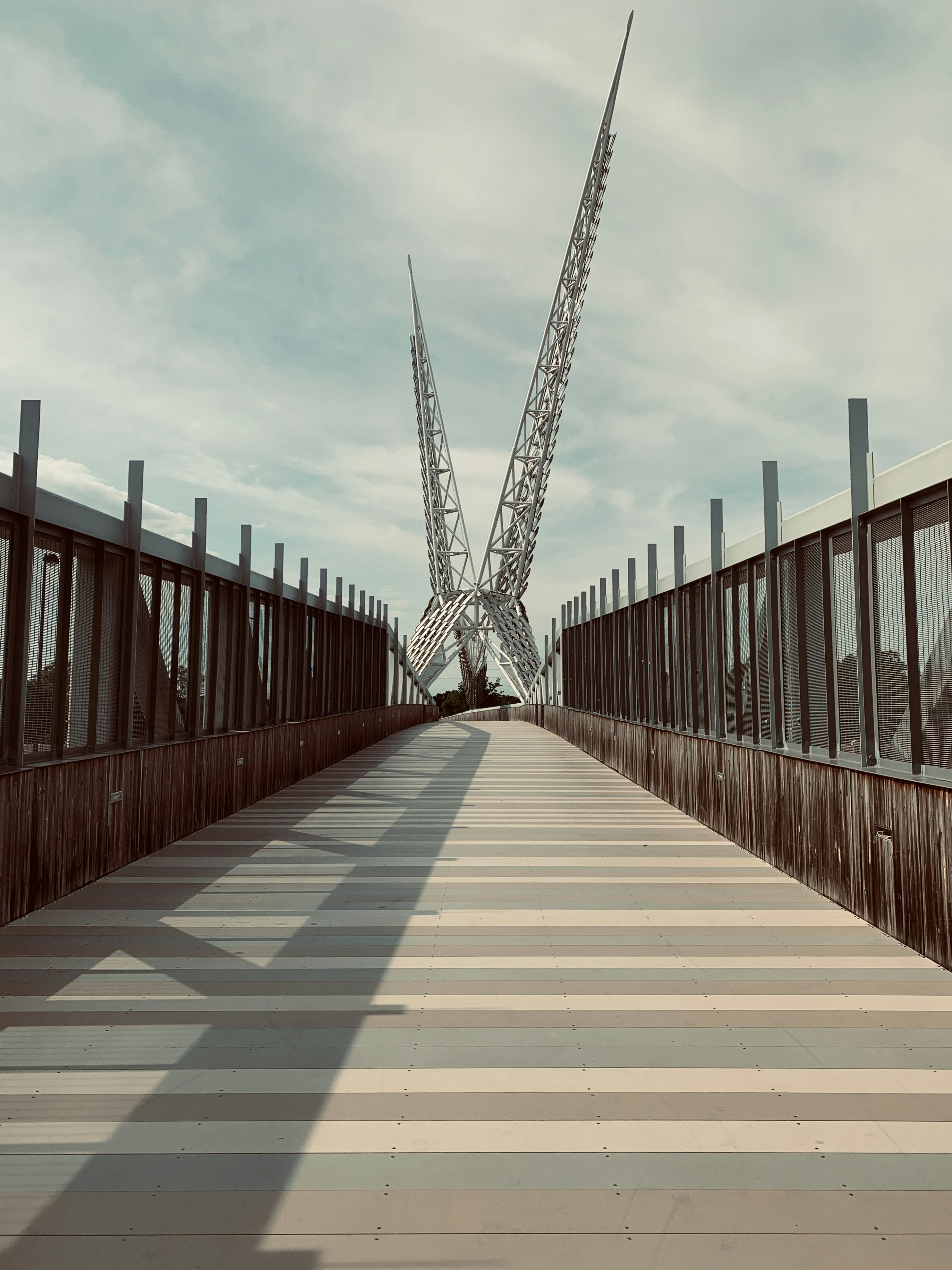 Modern bridge with striking angular supports leading towards a distant horizon. The wooden pathway creates a sense of depth and perspective.