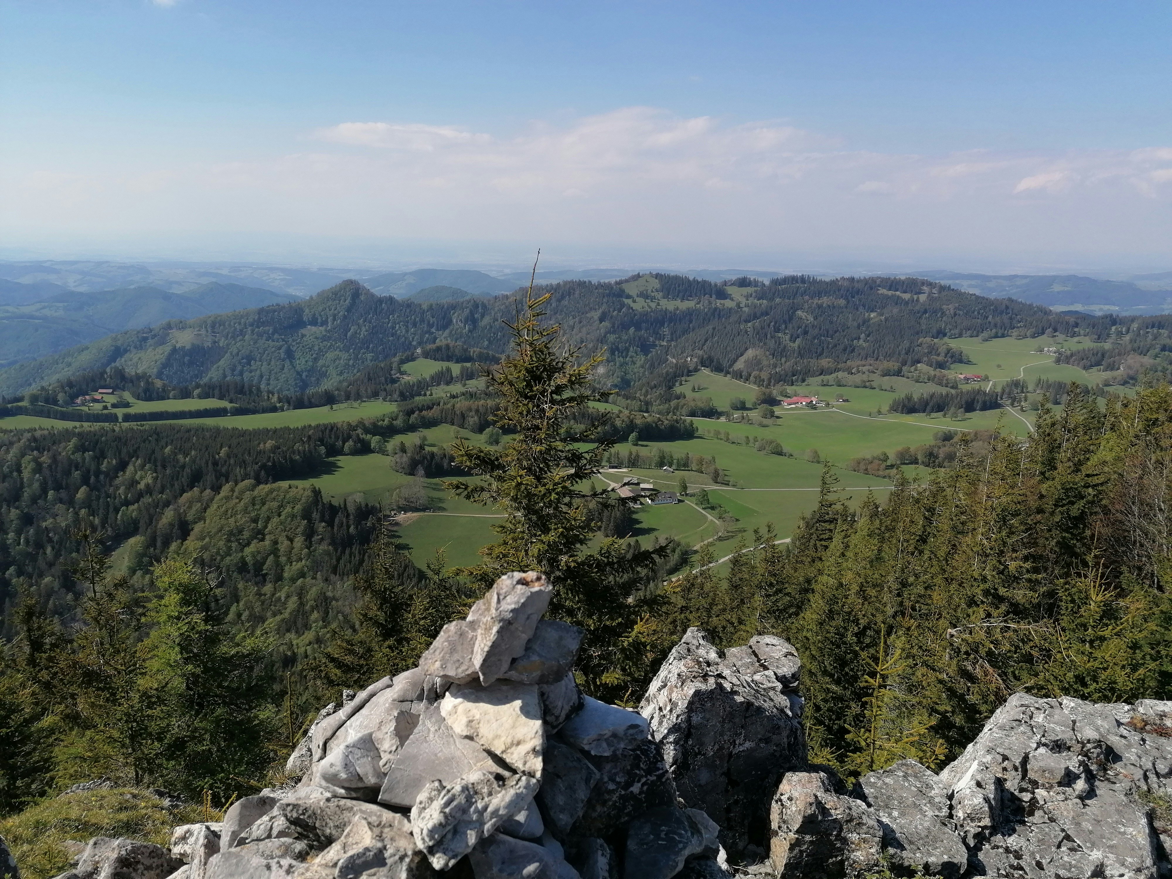 Panoramic view from a rocky outcrop showcasing lush green fields and rolling hills under a clear blue sky.