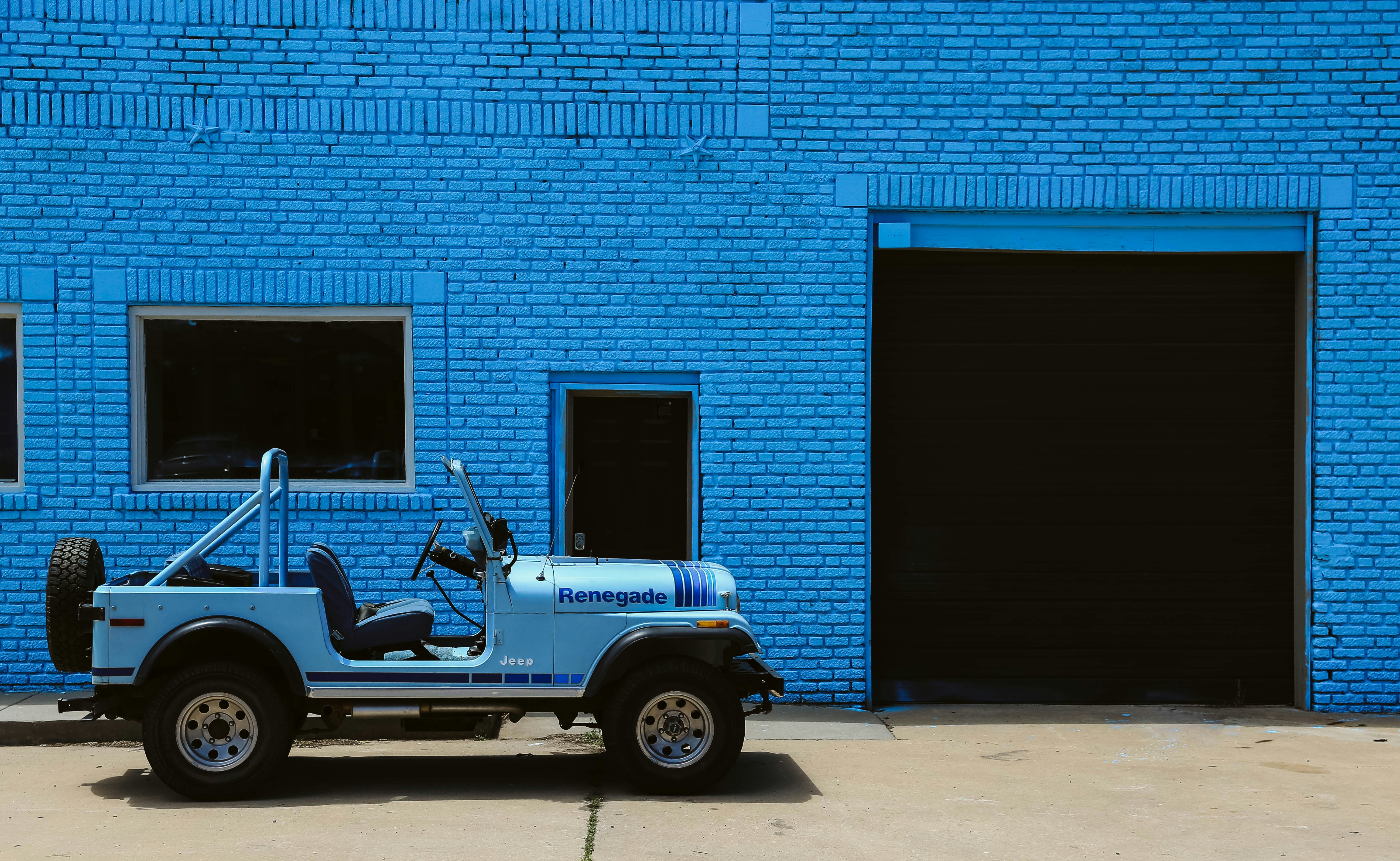 Light blue Jeep Renegade parked beside a vivid blue brick wall with contrasting black garage door and windows.