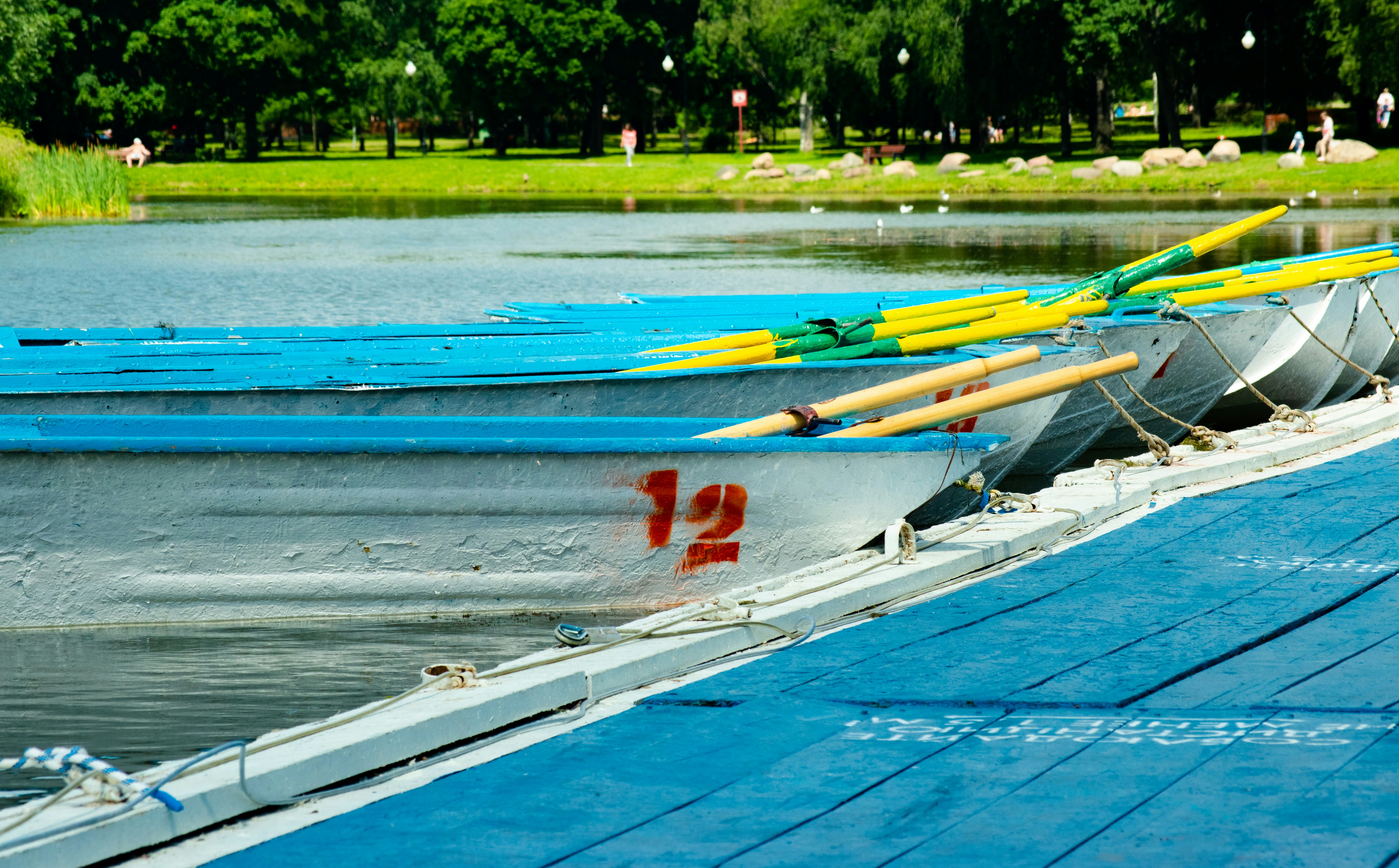Wooden rowboats with blue and yellow accents moored at a serene lake pier under vibrant green trees.
