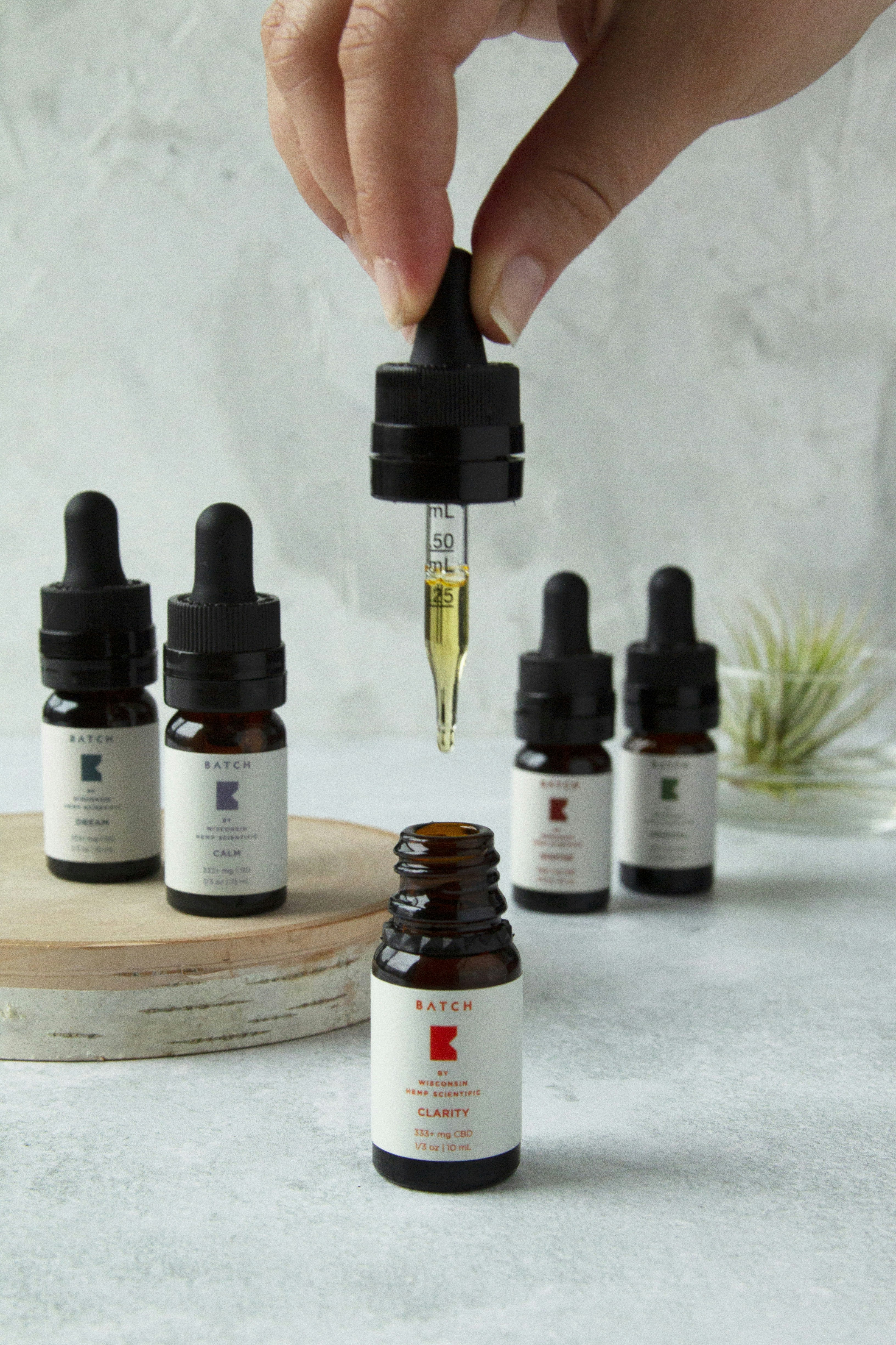 A hand delicately holds a dropper, releasing a golden liquid into a dark bottle labeled 'Clarity,' surrounded by various essential oil bottles on a wooden surface.