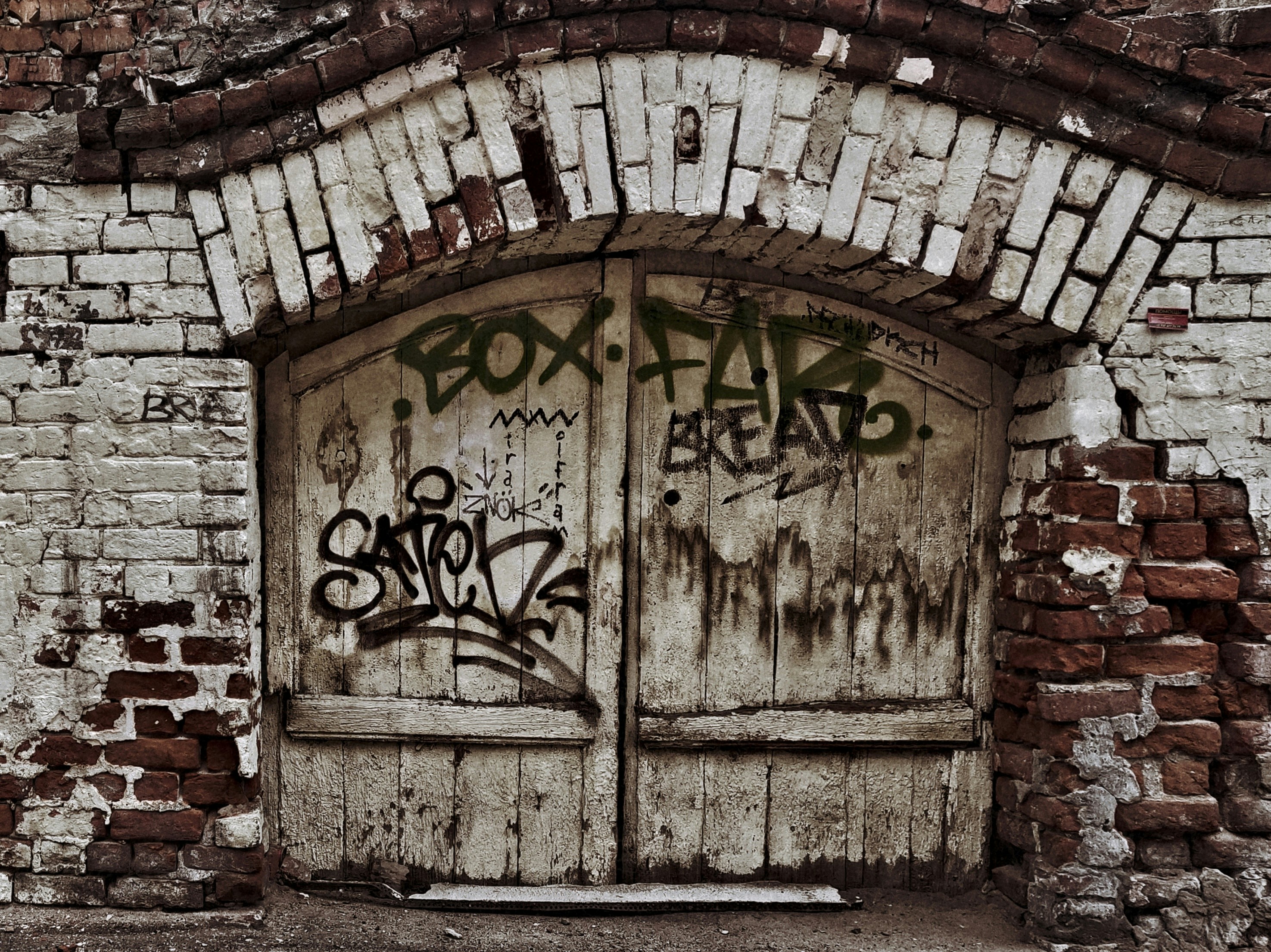 Crumbled Arch Gate: Graffiti Adorns a Weathered Brick Façade